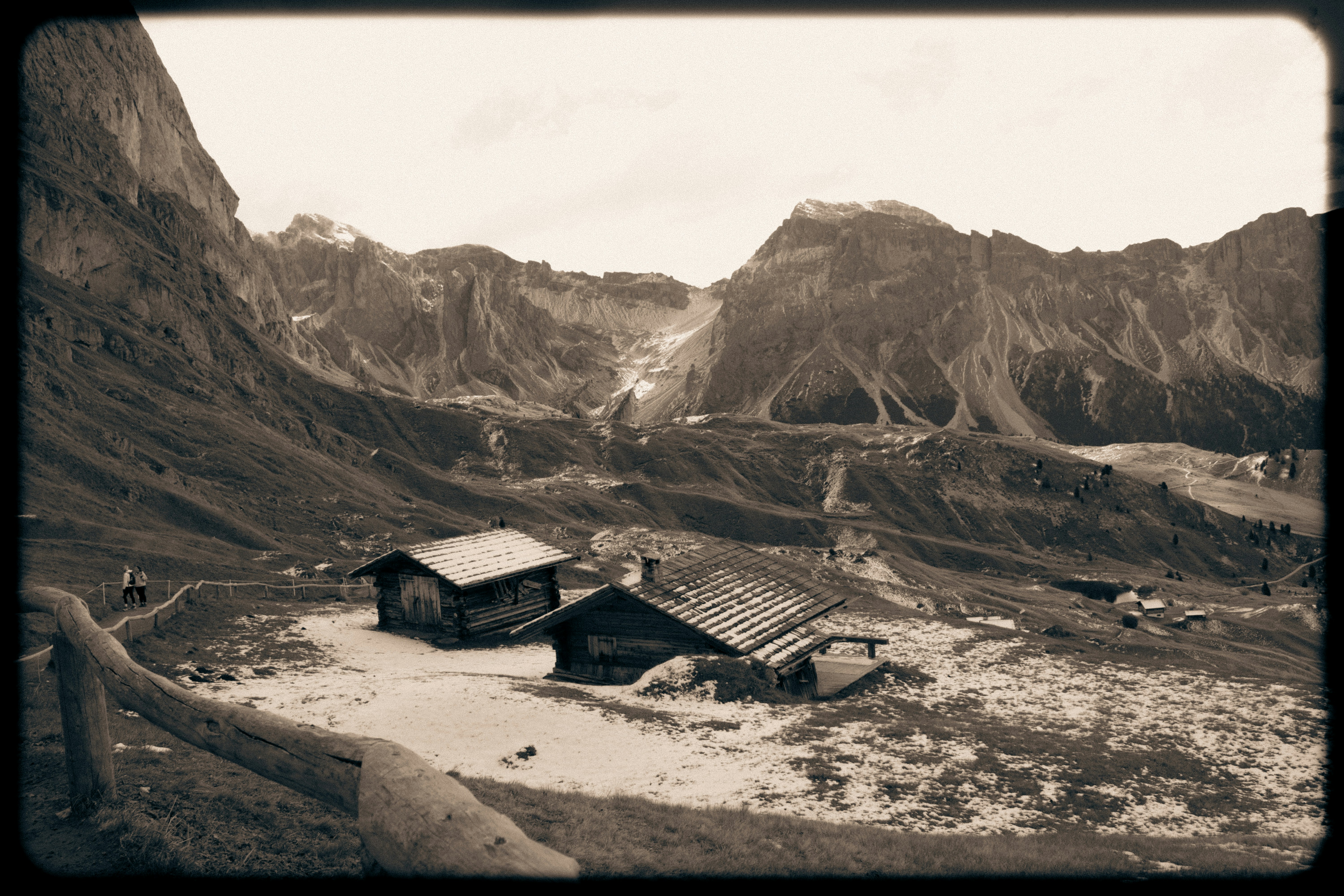 Two old wooden huts in a sepia-toned mountain landscape.