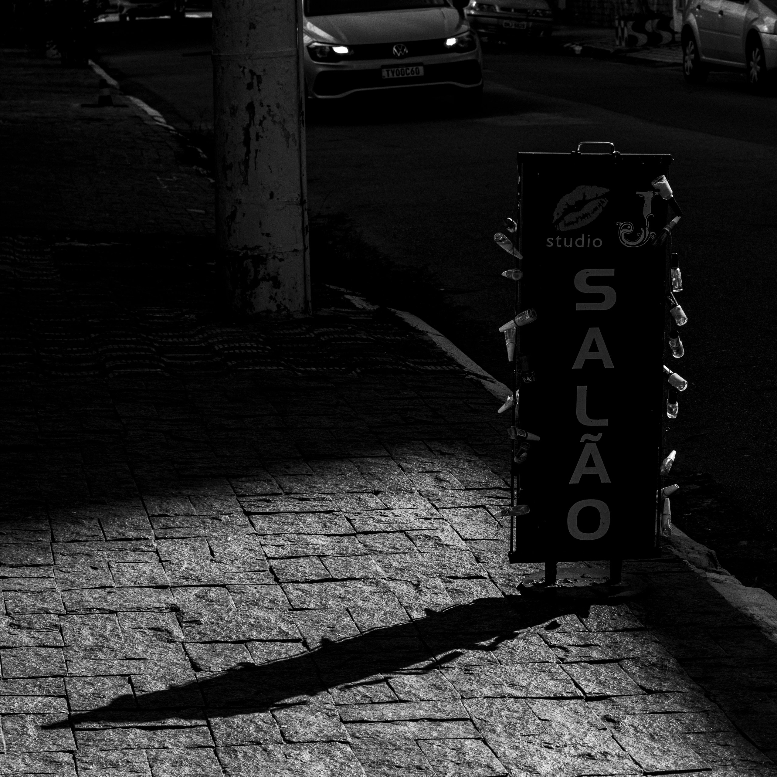 A "studio" sign with nail polish bottles hangs on a sidewalk at night, casting a long shadow.