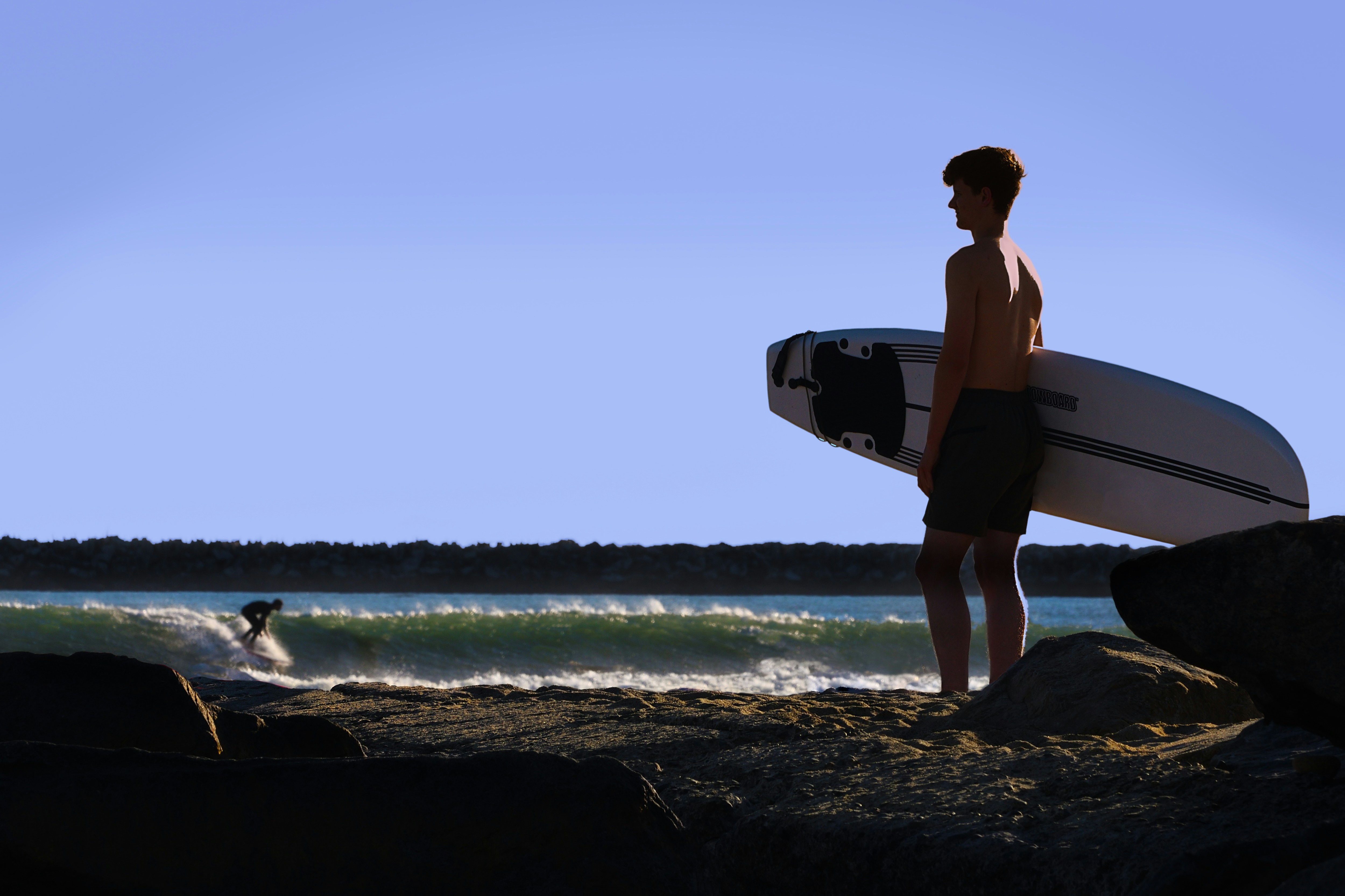 Silhouette at the Shore: Surfer With a White Board Against a Blue Horizon