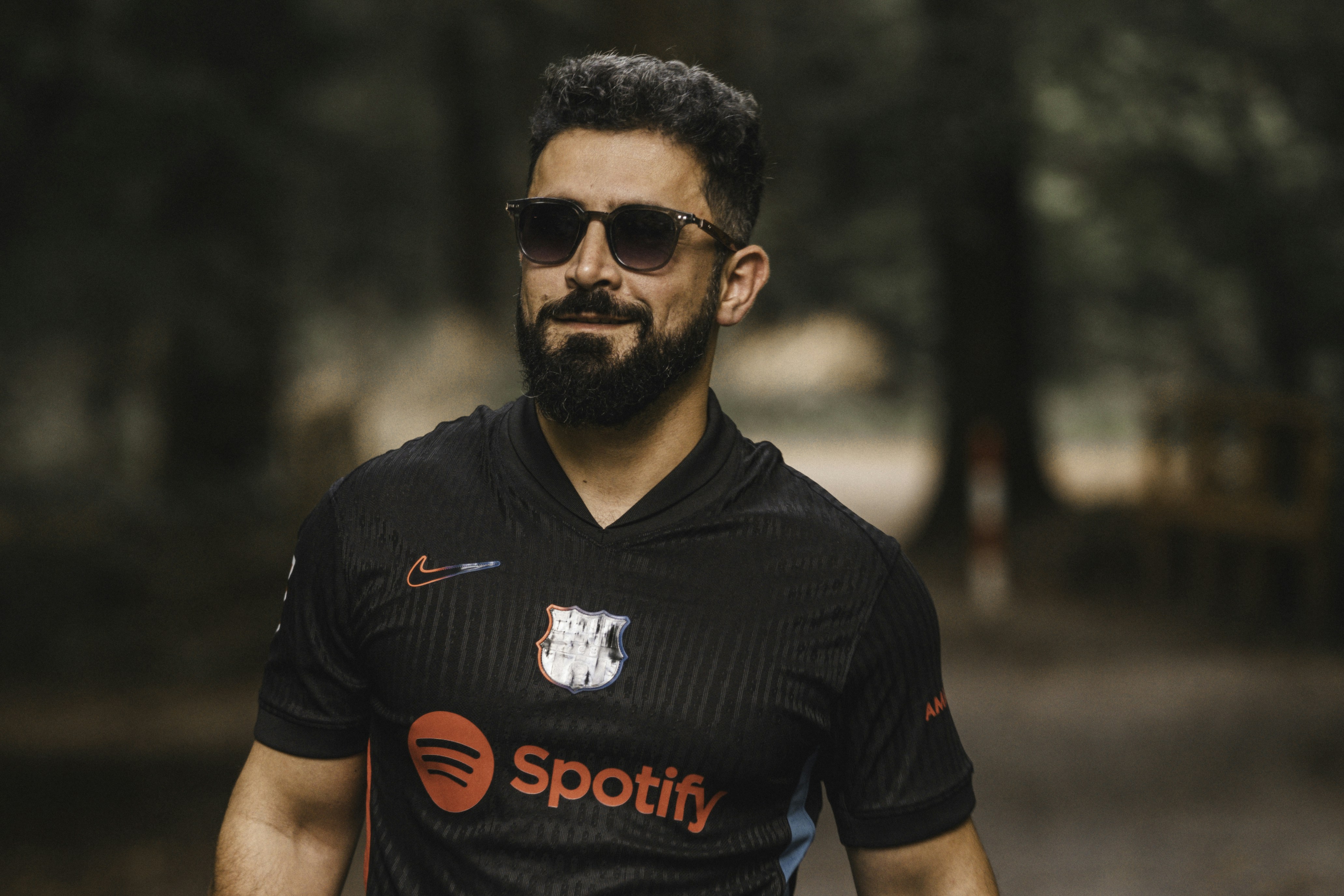Bearded man in sunglasses and black shirt outdoors.