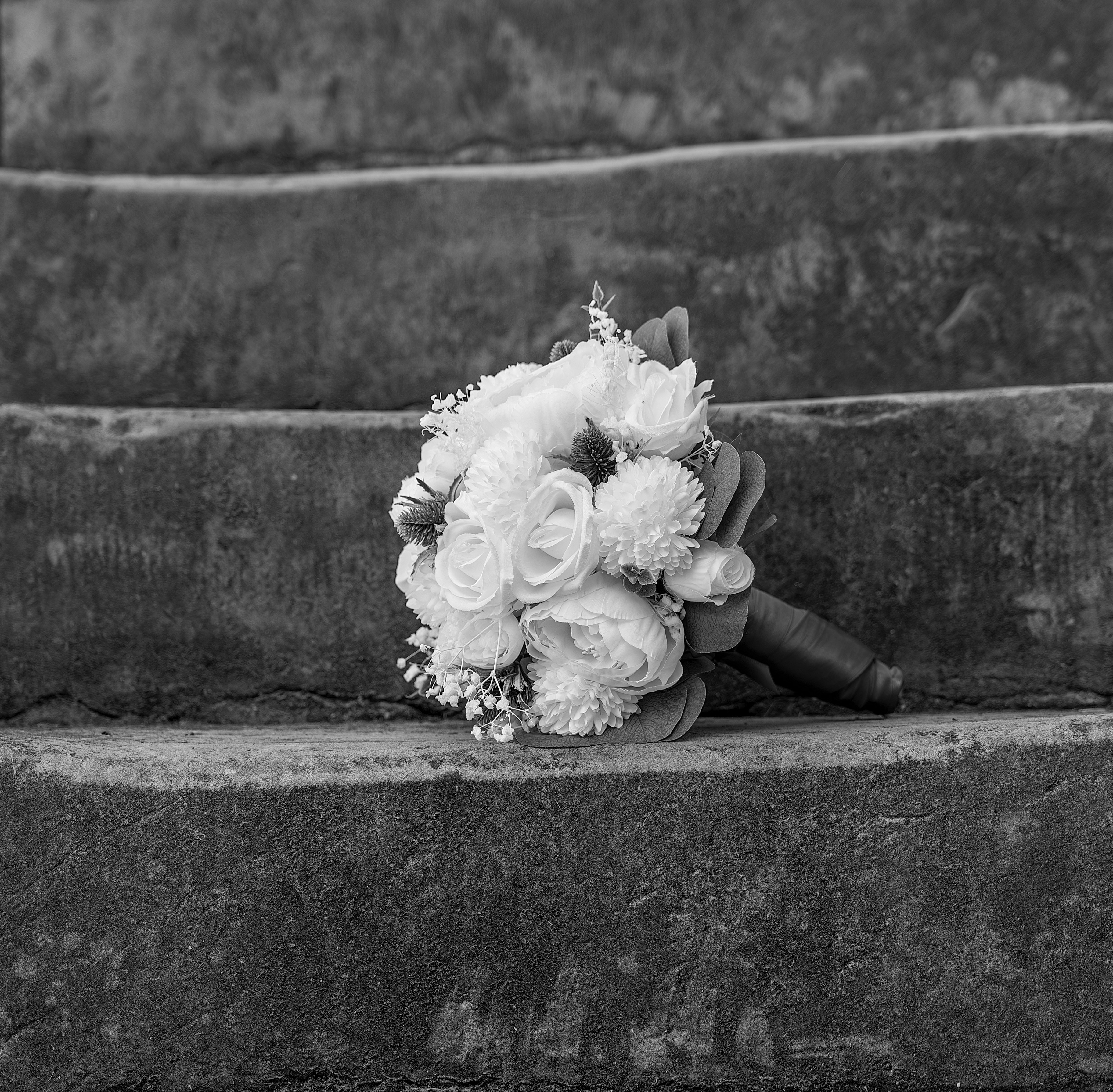 A monochrome bouquet rests on stone steps, its petals and greenery forming a delicate focal point against the textured backdrop.