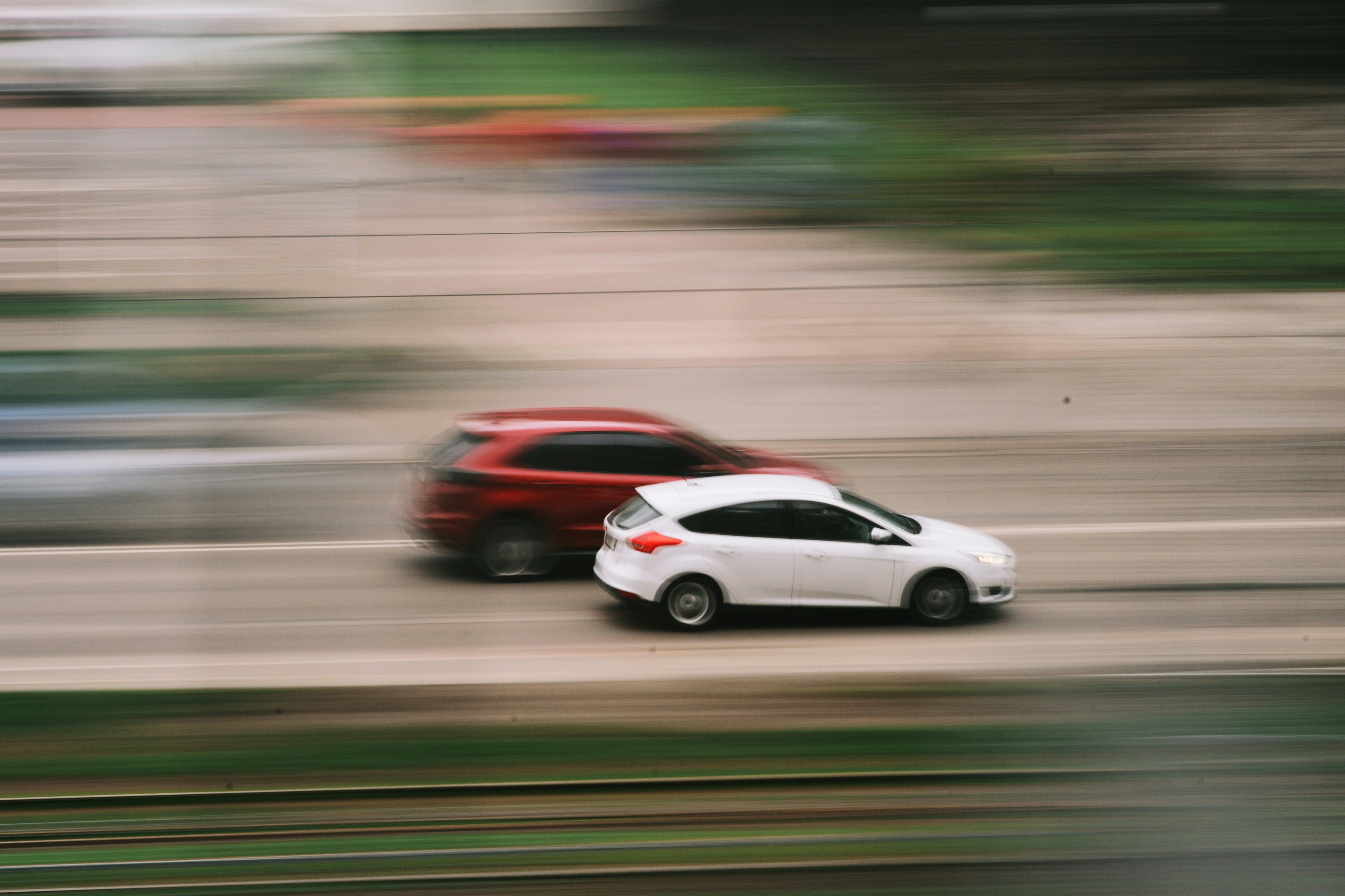 White sedan leads a blurred pair of vehicles on a highway, captured with motion blur that emphasizes speed and motion.
