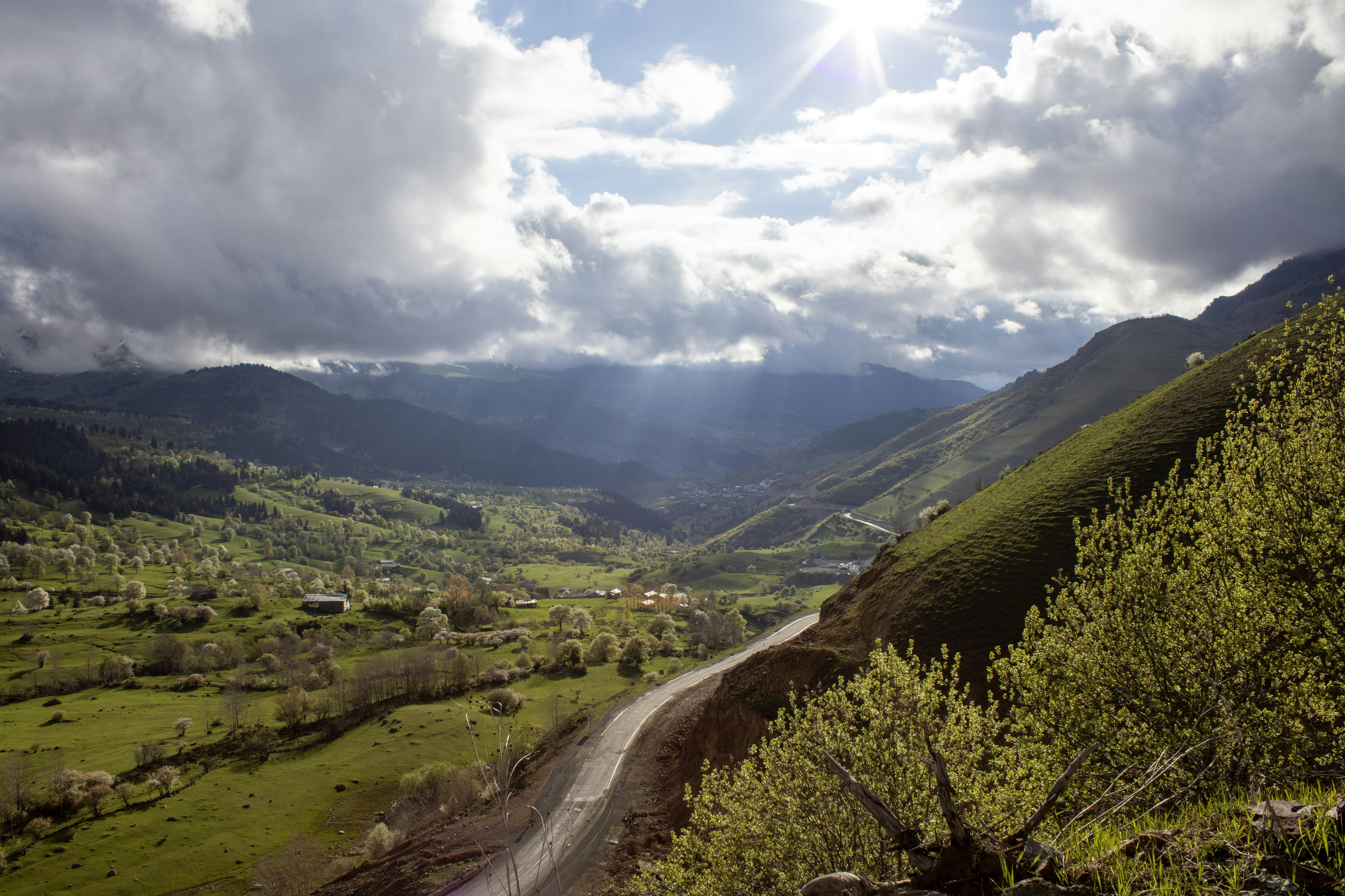 Sunlit valley emerges from rolling hills under dramatic clouds