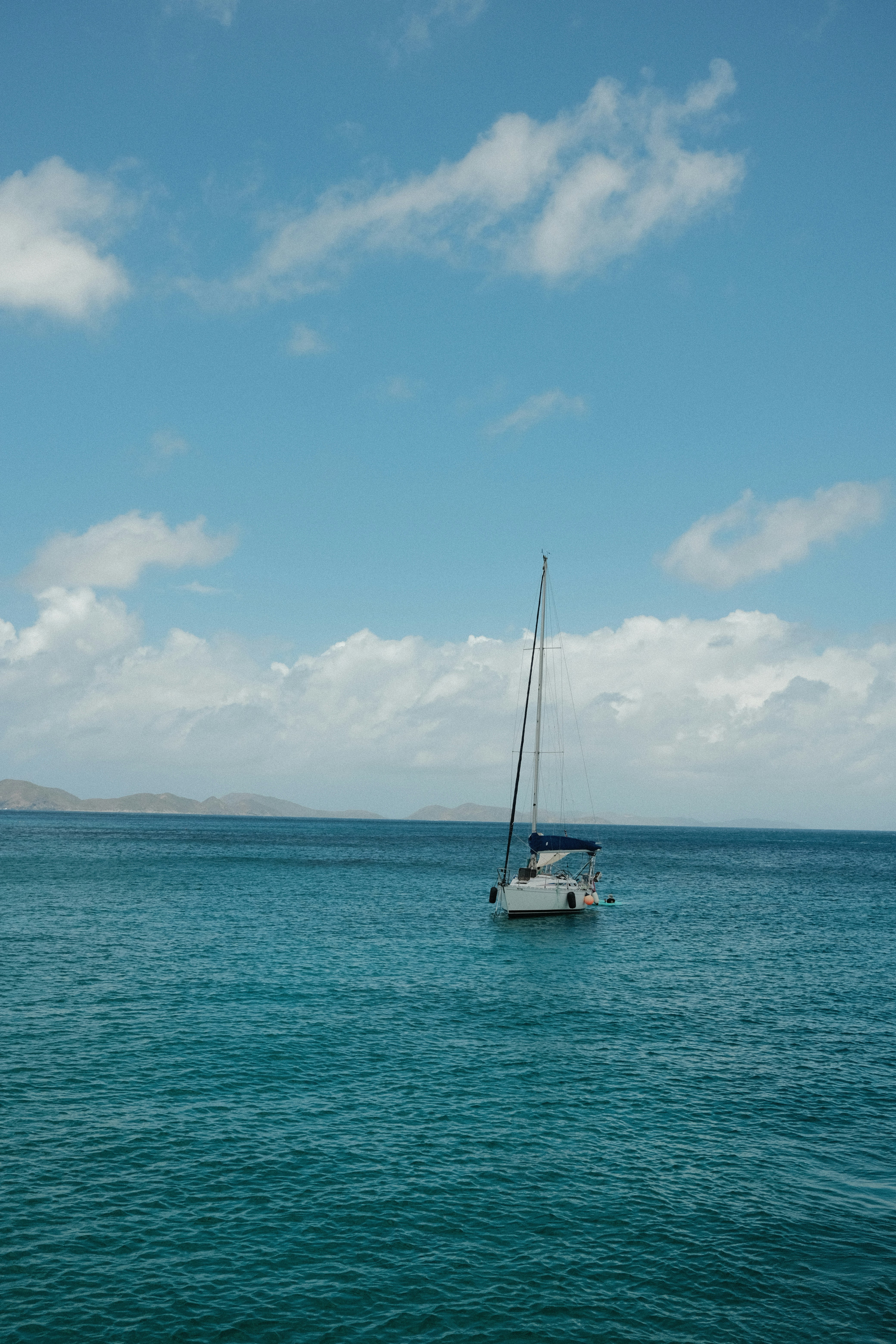 Sailboat rests on calm turquoise sea under a bright, airy sky with scattered clouds.