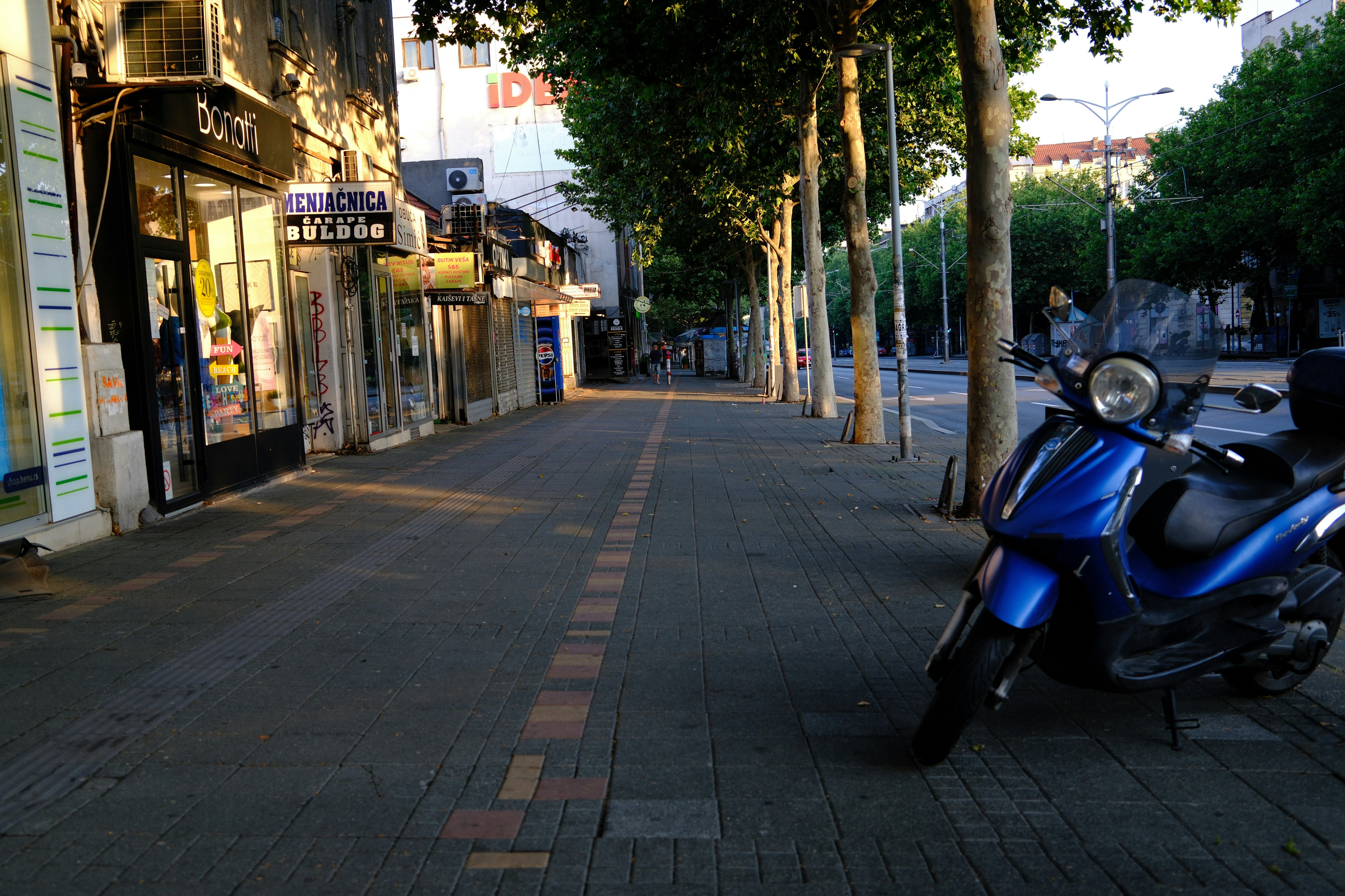 Blue Scooter at the Edge of a Sunlit City Street