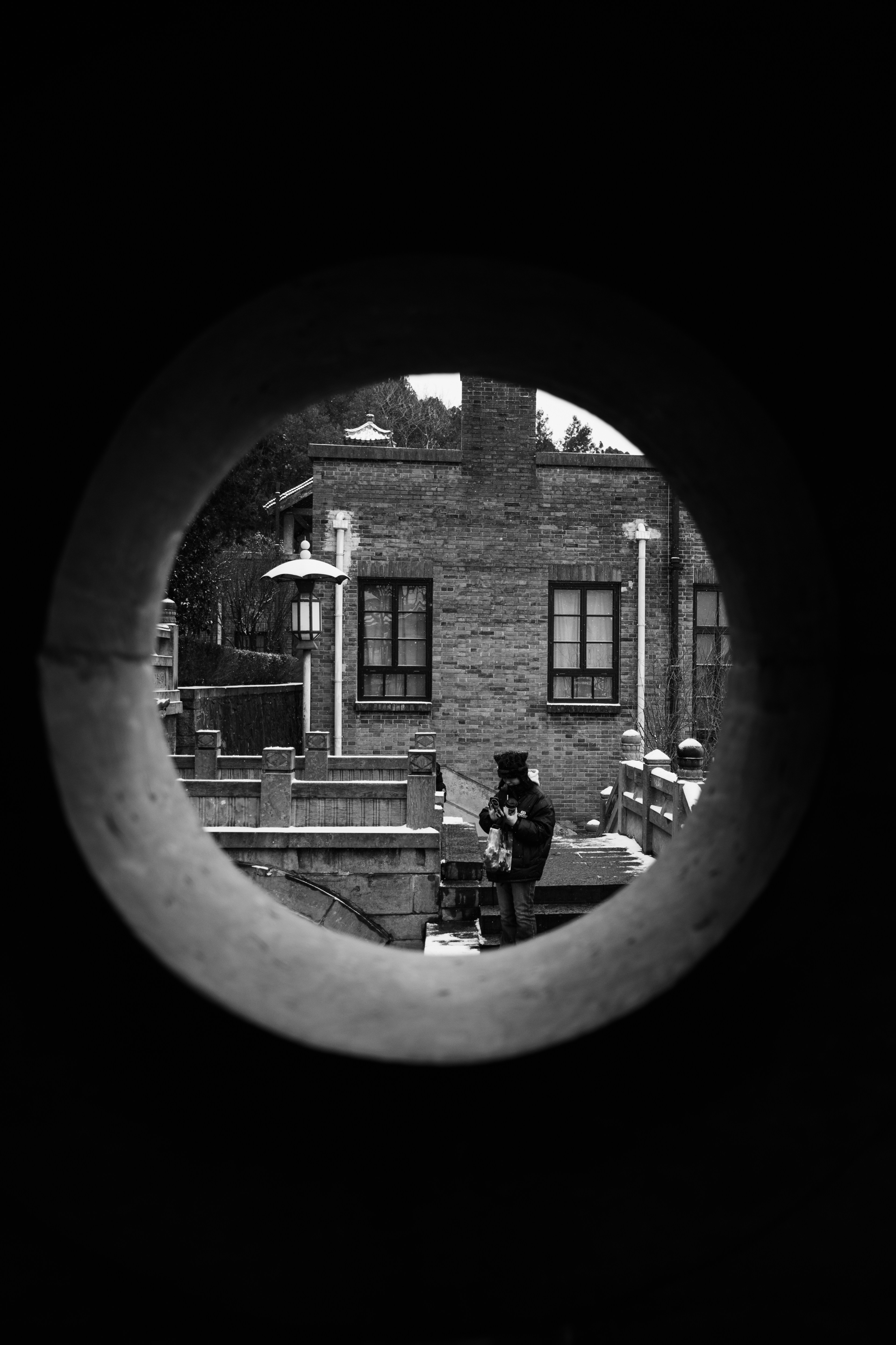 Through a Circular Window: A Quiet Figure in a Brick Courtyard
