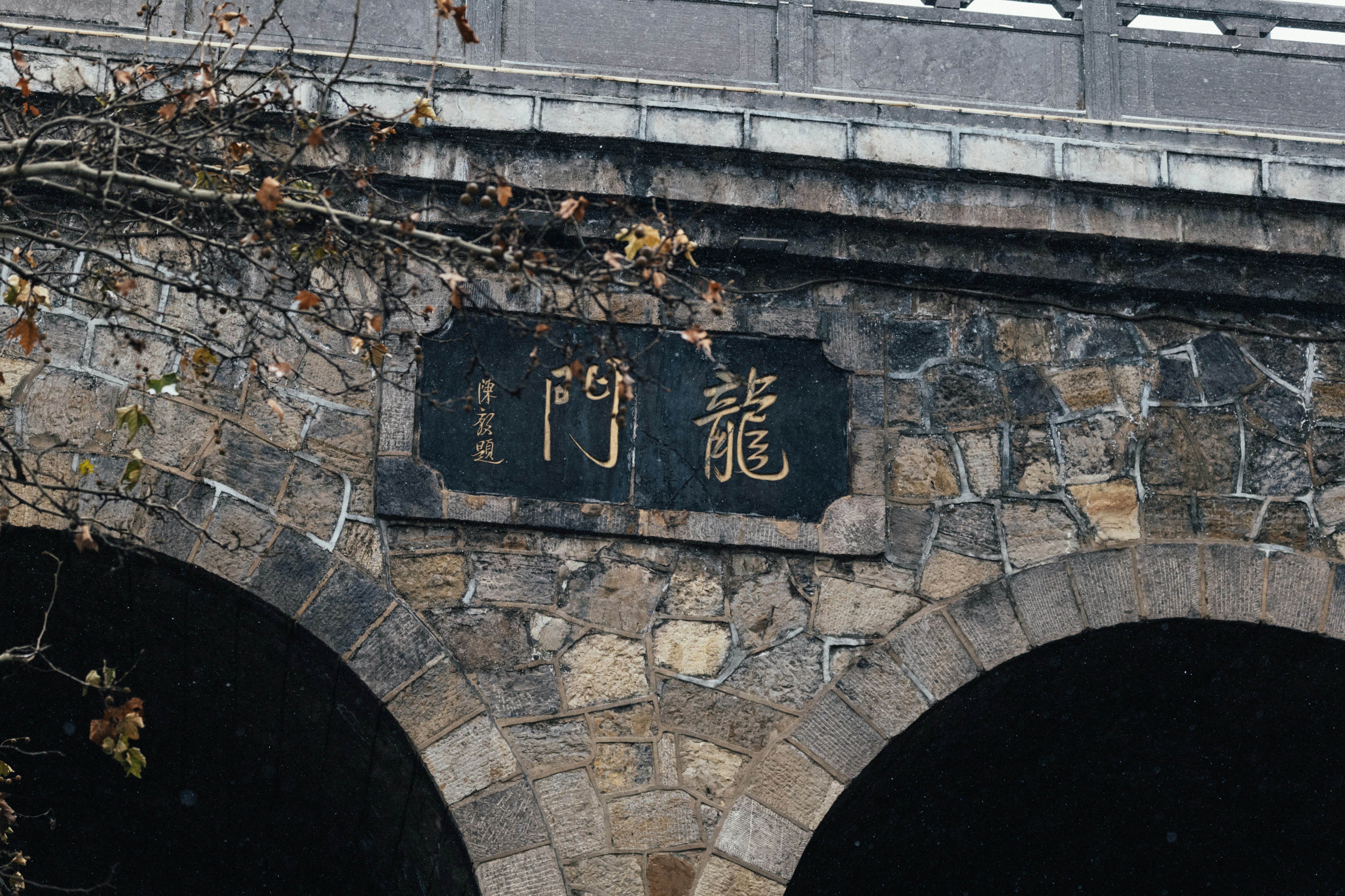 Stone Archway with Inscribed Panels under a Weathered Bridge