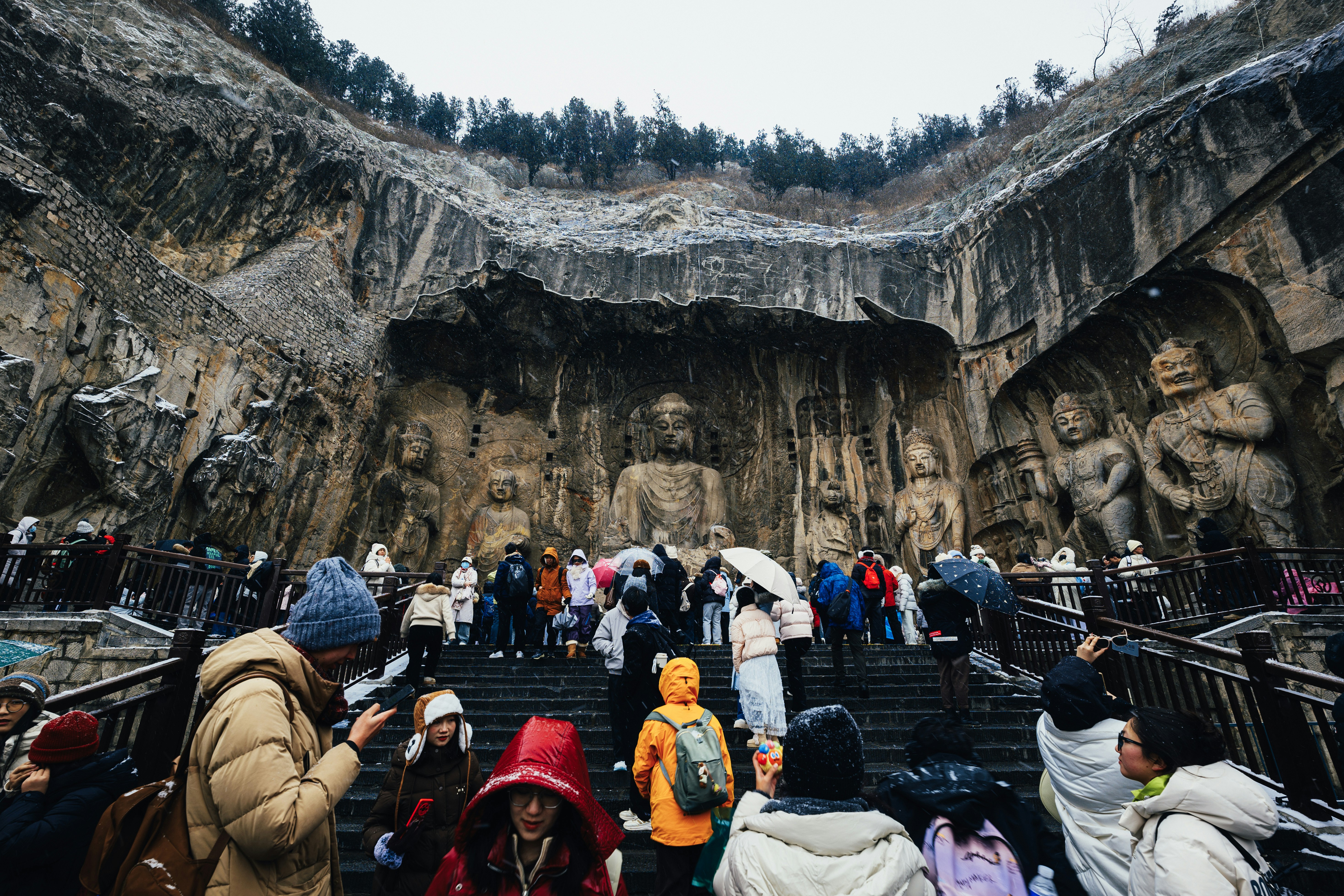 Crowded ascent beneath a carved cliffside of Buddha statues