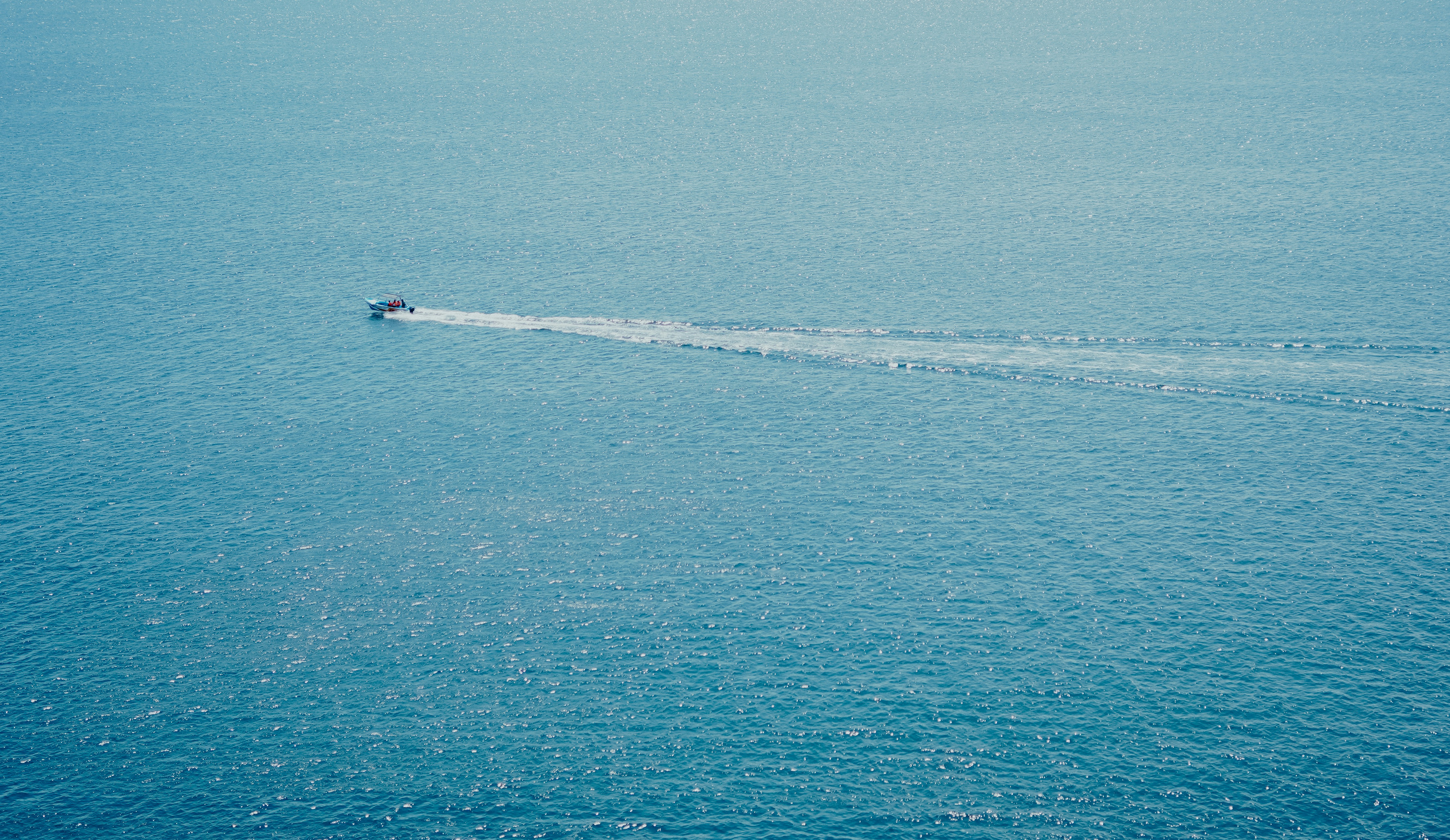 A lone motorboat cuts a white wake across a vast blue sea