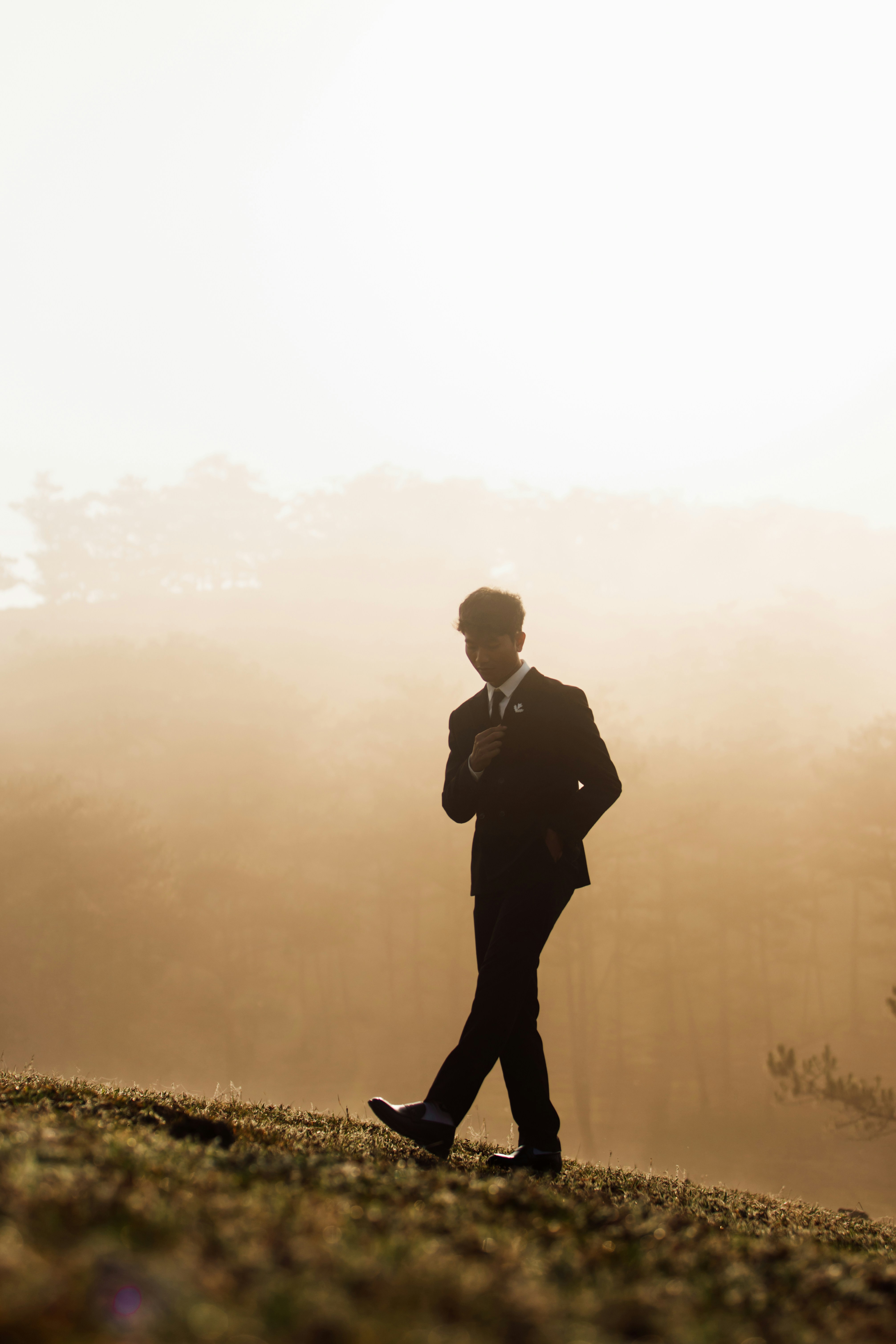 A solitary silhouette of a man in a suit walking on a sunlit, misty hillside; the scene emphasizes mood and form with soft backlight. This is a photography-based capture, not a painting or illustration.