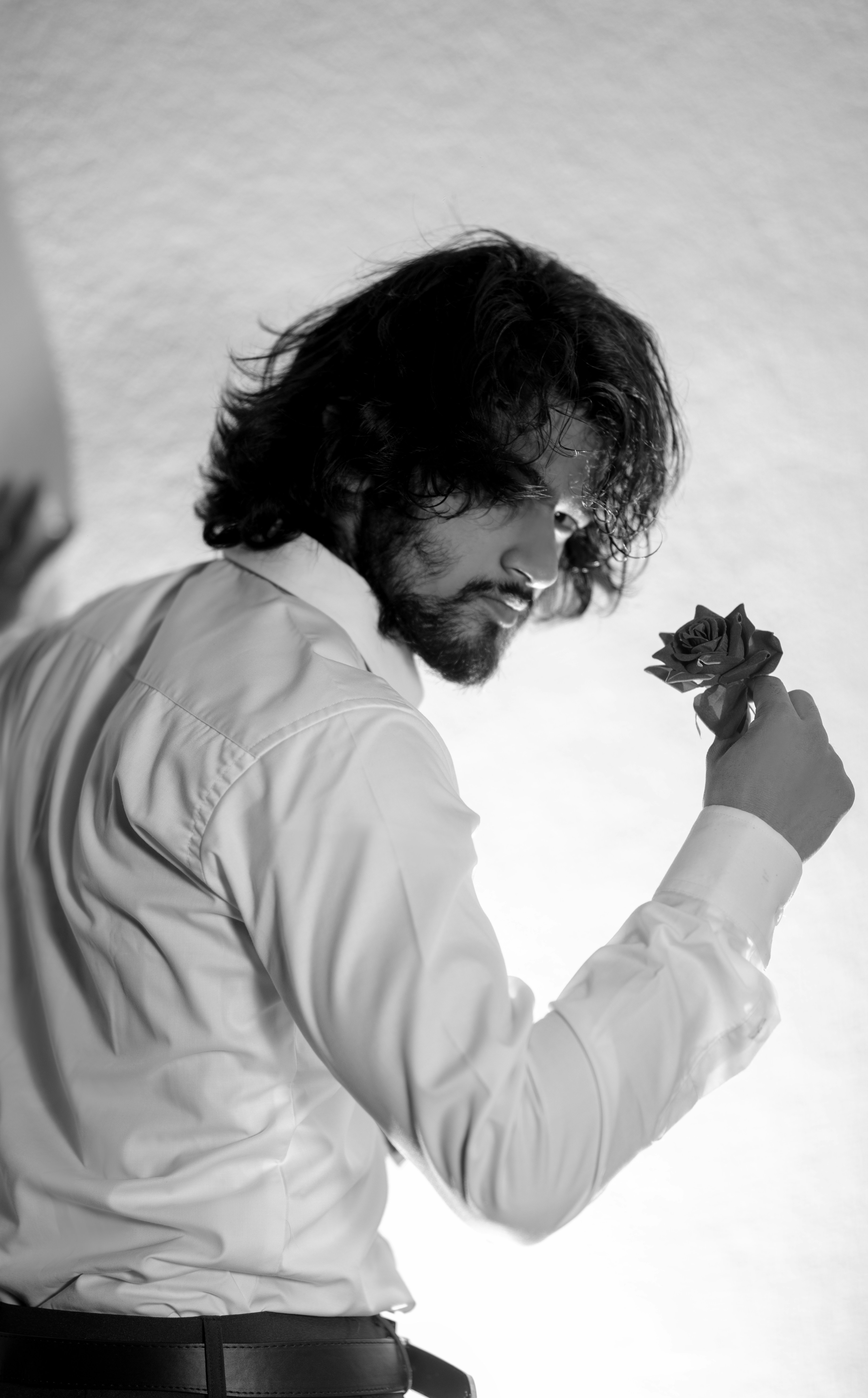 “A stylish young man with flowing dark hair and a well-groomed beard stands against a soft neutral backdrop. Dressed in a crisp white shirt and elegant gray tie, he adjusts his cuff with calm confidence. His windswept hair and contemplative expression create a captivating blend of sophistication and mystery, while the soft lighting enhances the portrait’s cinematic and fashion-inspired appeal.” ✨📸