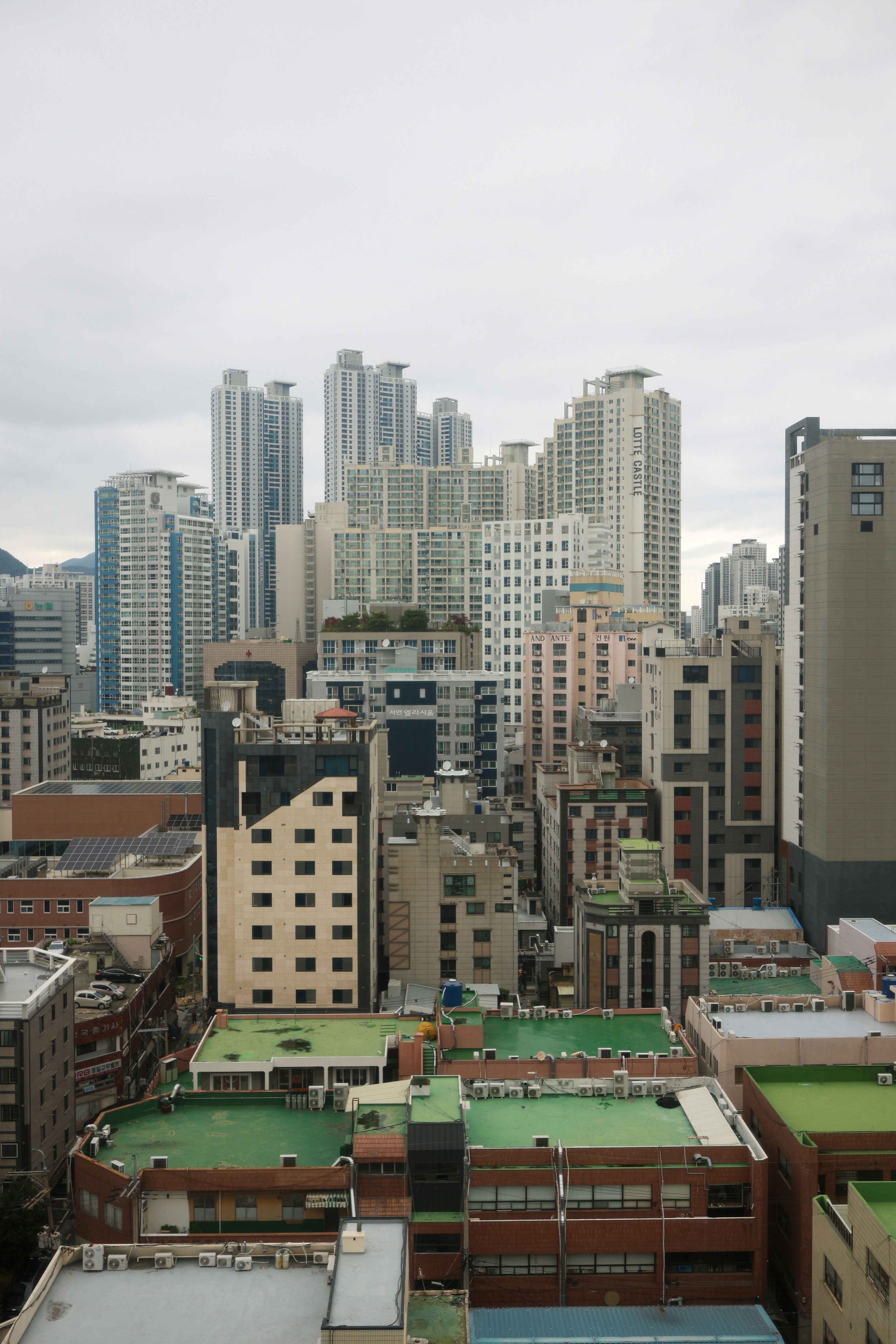 Dense urban skyline with mid- and high-rise buildings rising above lower blocks, topped by a gray, overcast sky.