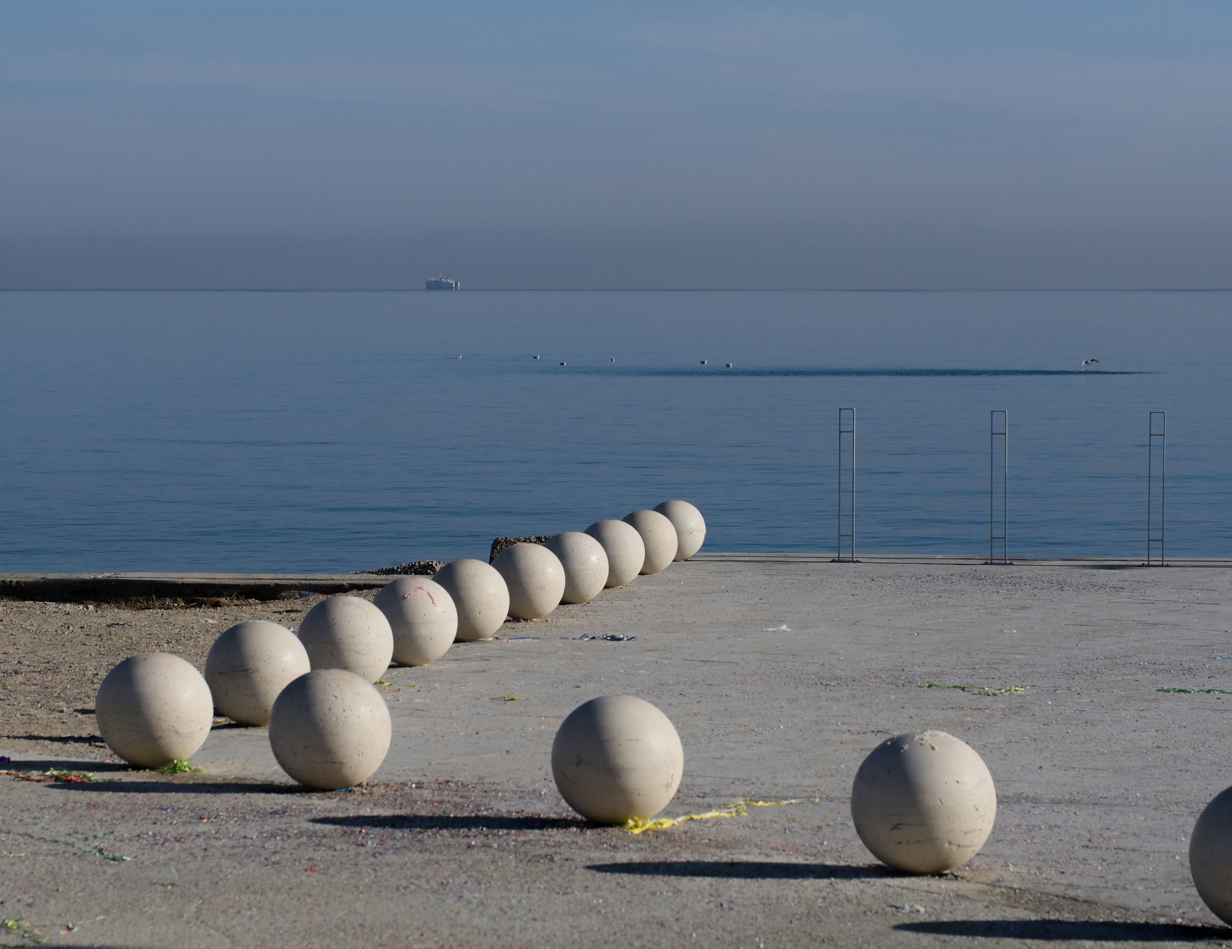 Row of Concrete Spheres Recedes Toward Calm Sea Horizon