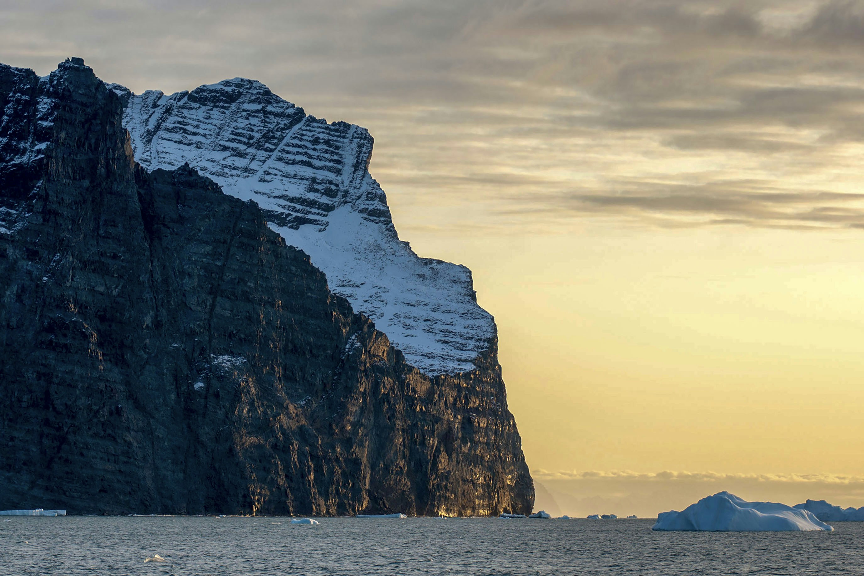Sunlit Cliff Edge Over Calm Arctic Waters at Dusk