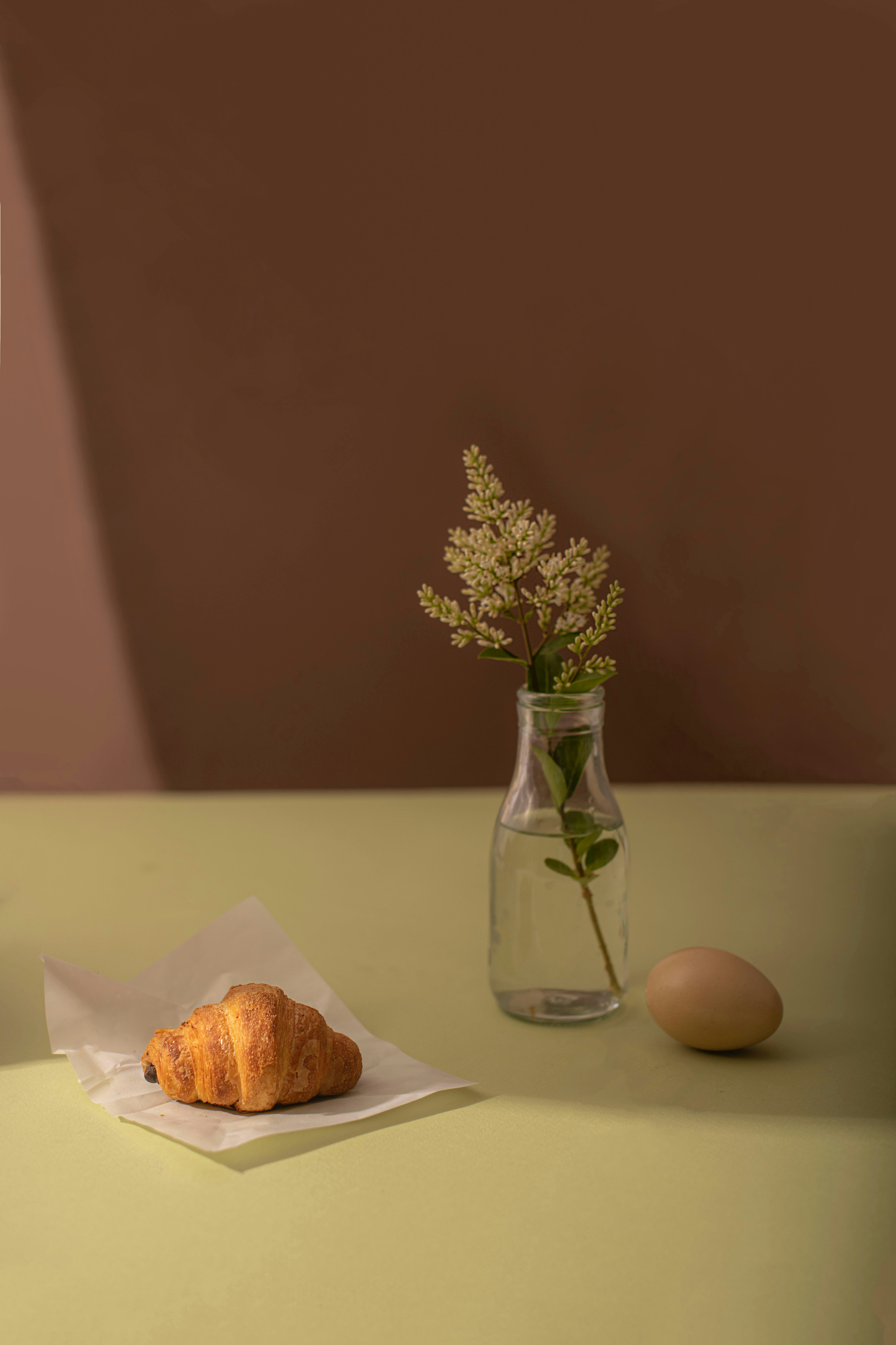 Quiet Morning Still-Life: Croissant, Egg, and Stemmed Flower in Glass Bottle