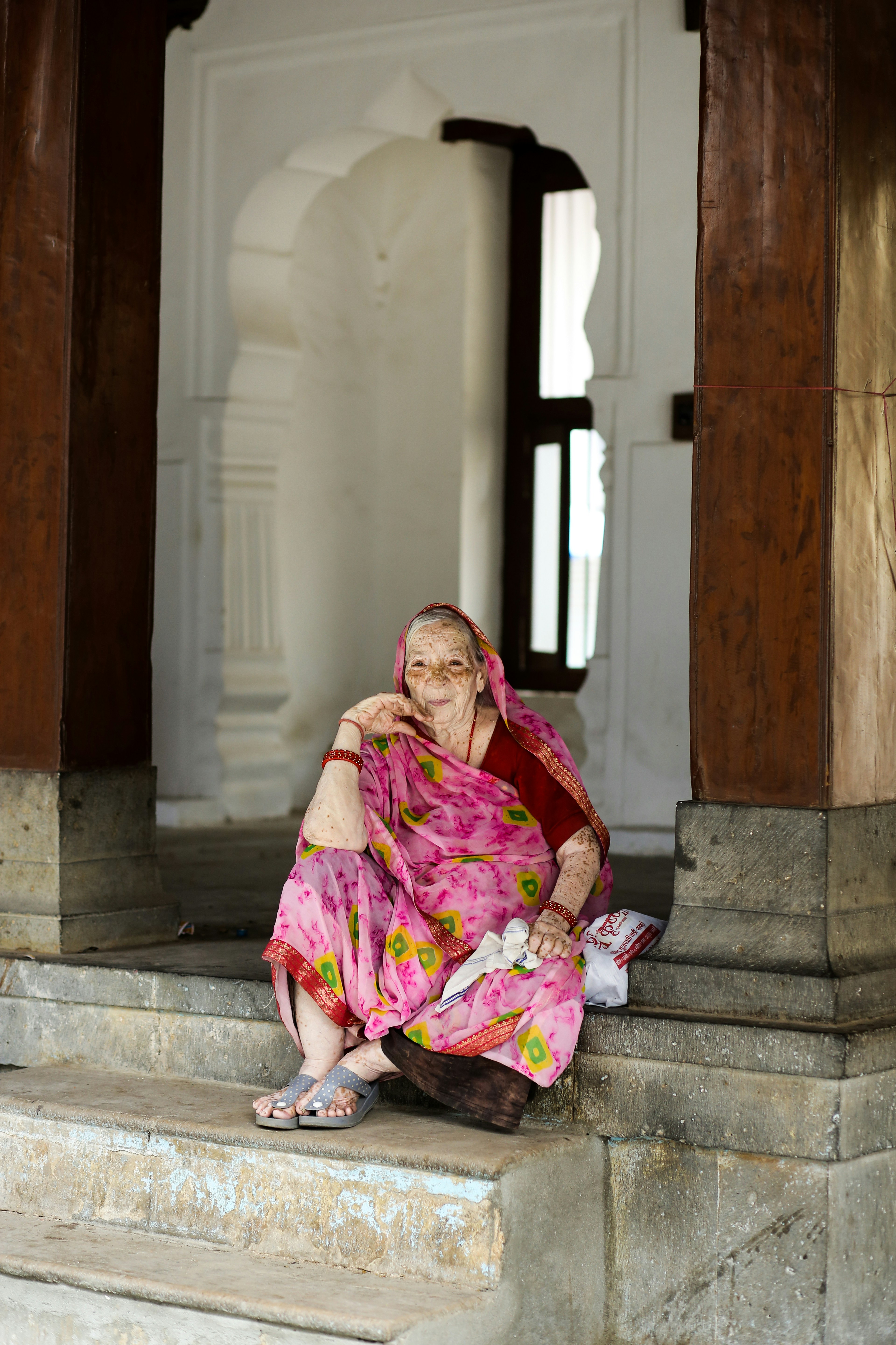 Heritage Porch Moment: Elderly Woman in Pink Saree Sits Quietly on Stone Steps