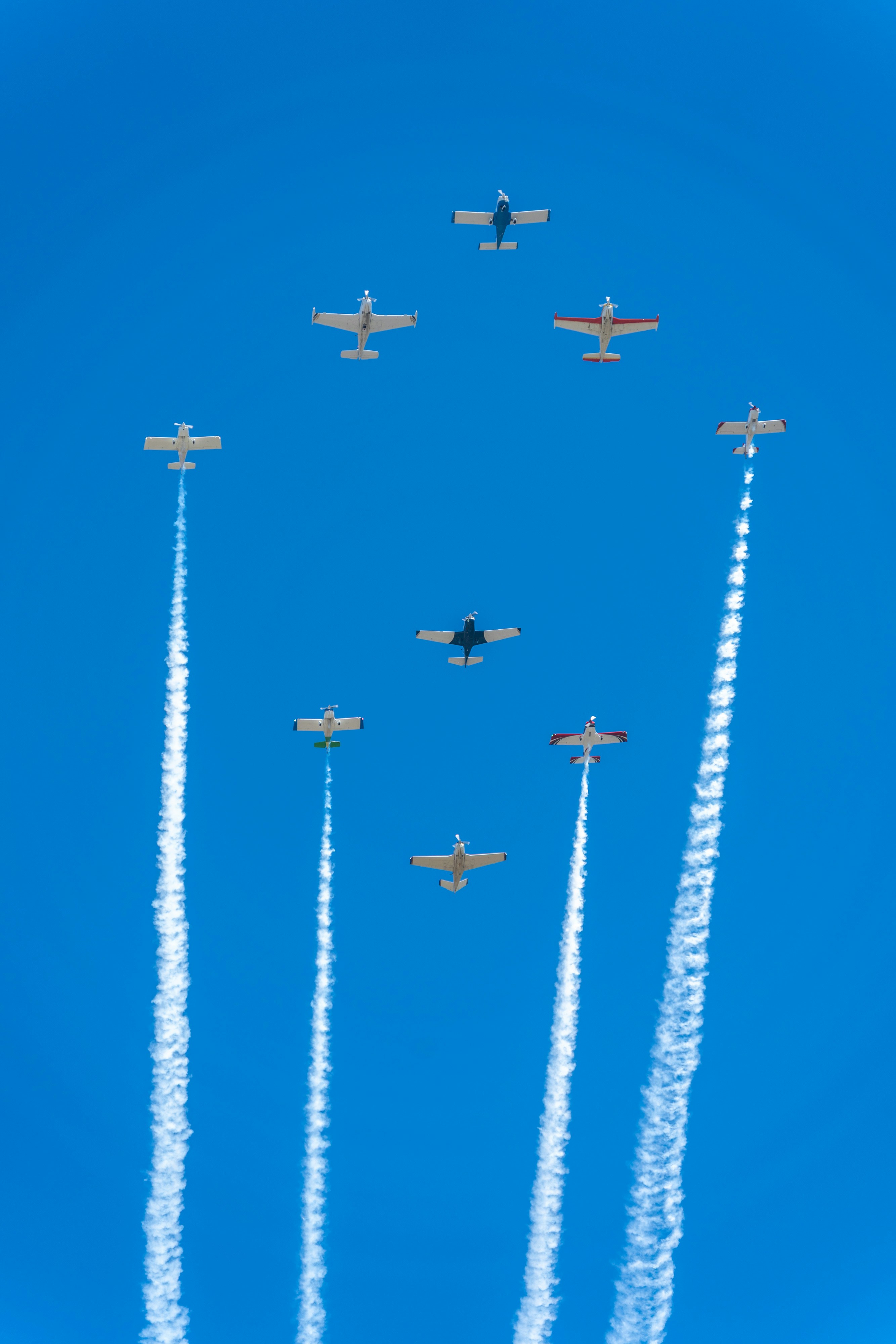 Nine airplanes flying in formation leaving white smoke trails.
