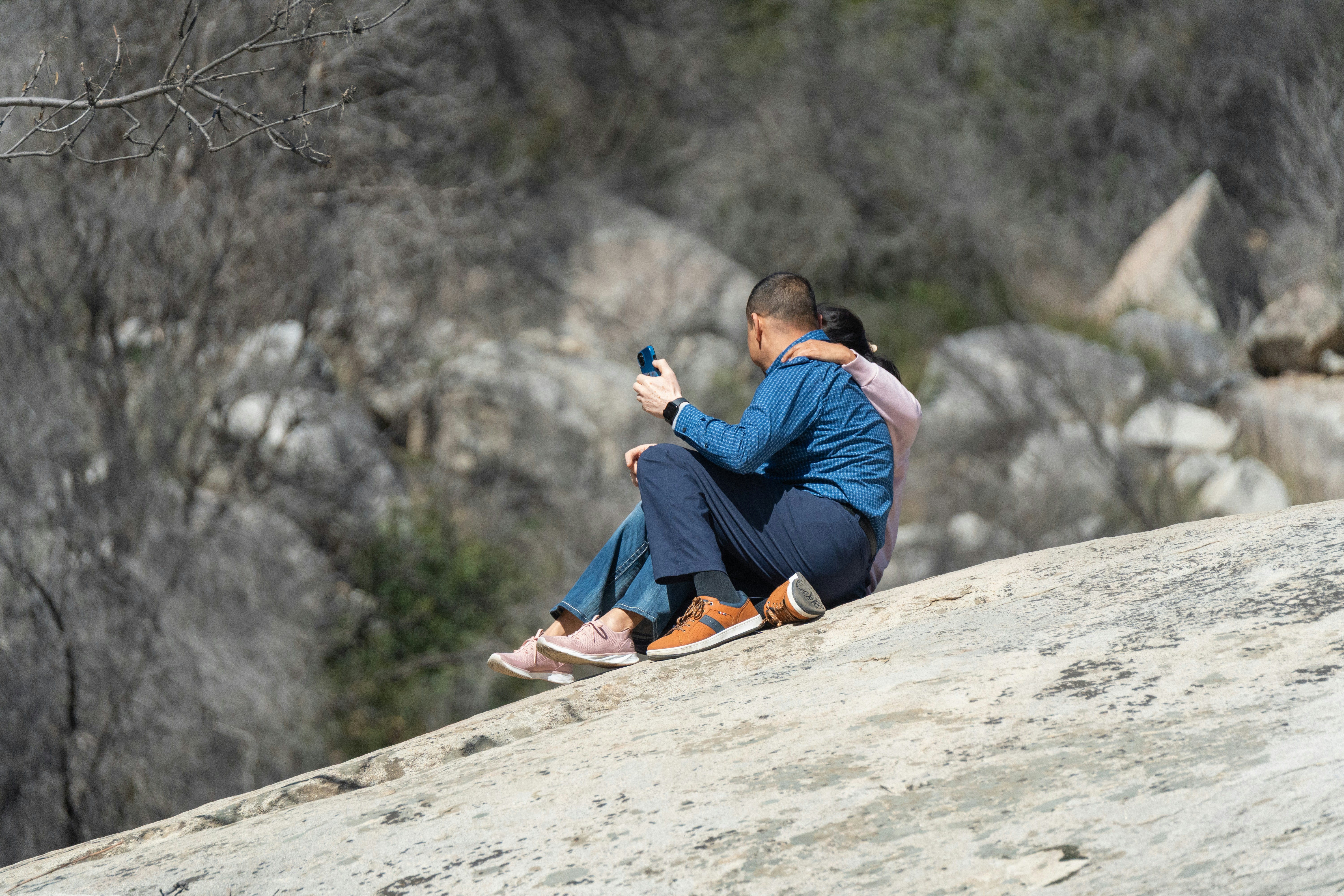 Two hikers on a sunlit, sloped rock with a phone moment