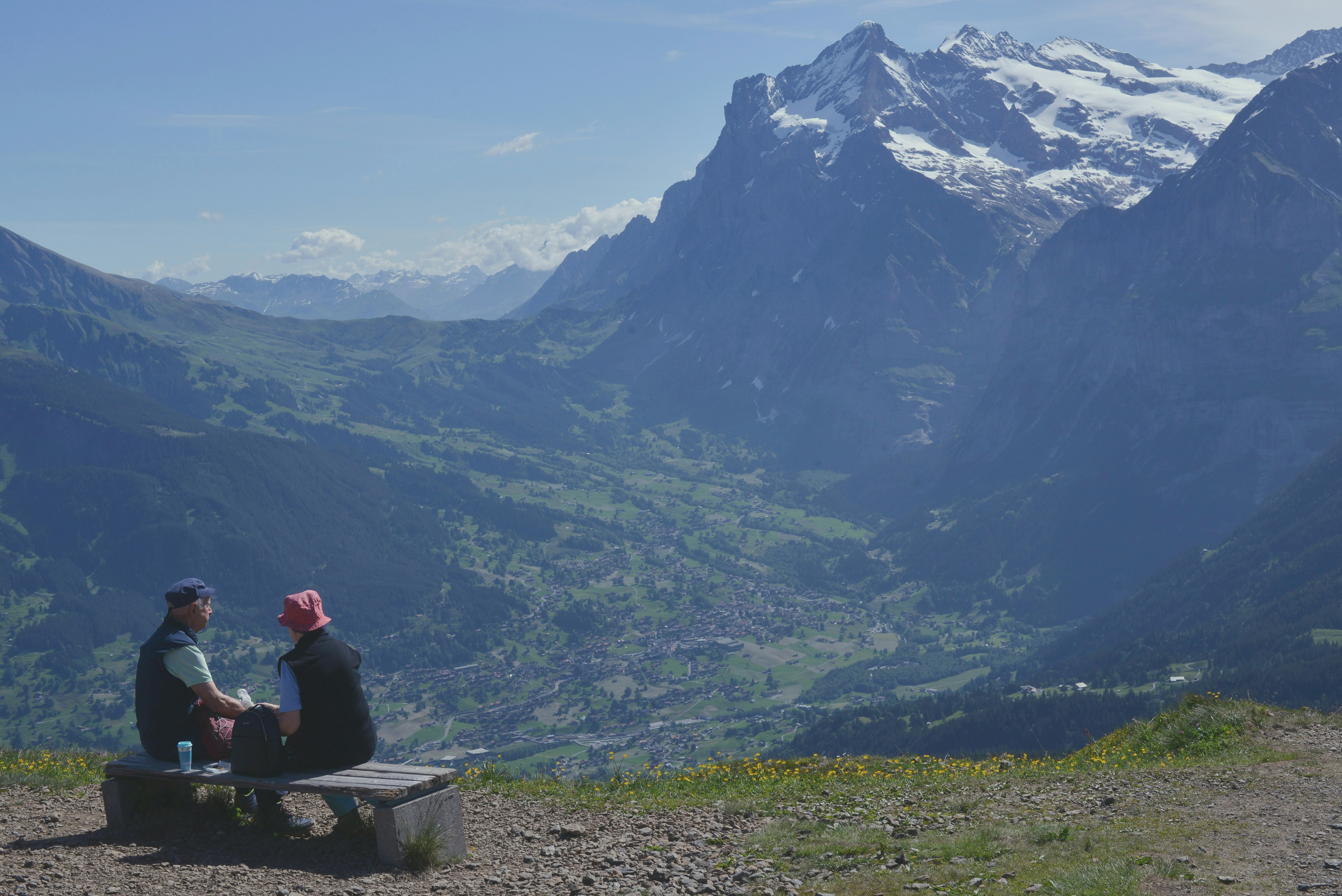 Two hikers resting on a valley overlook beneath snow-dusted peaks