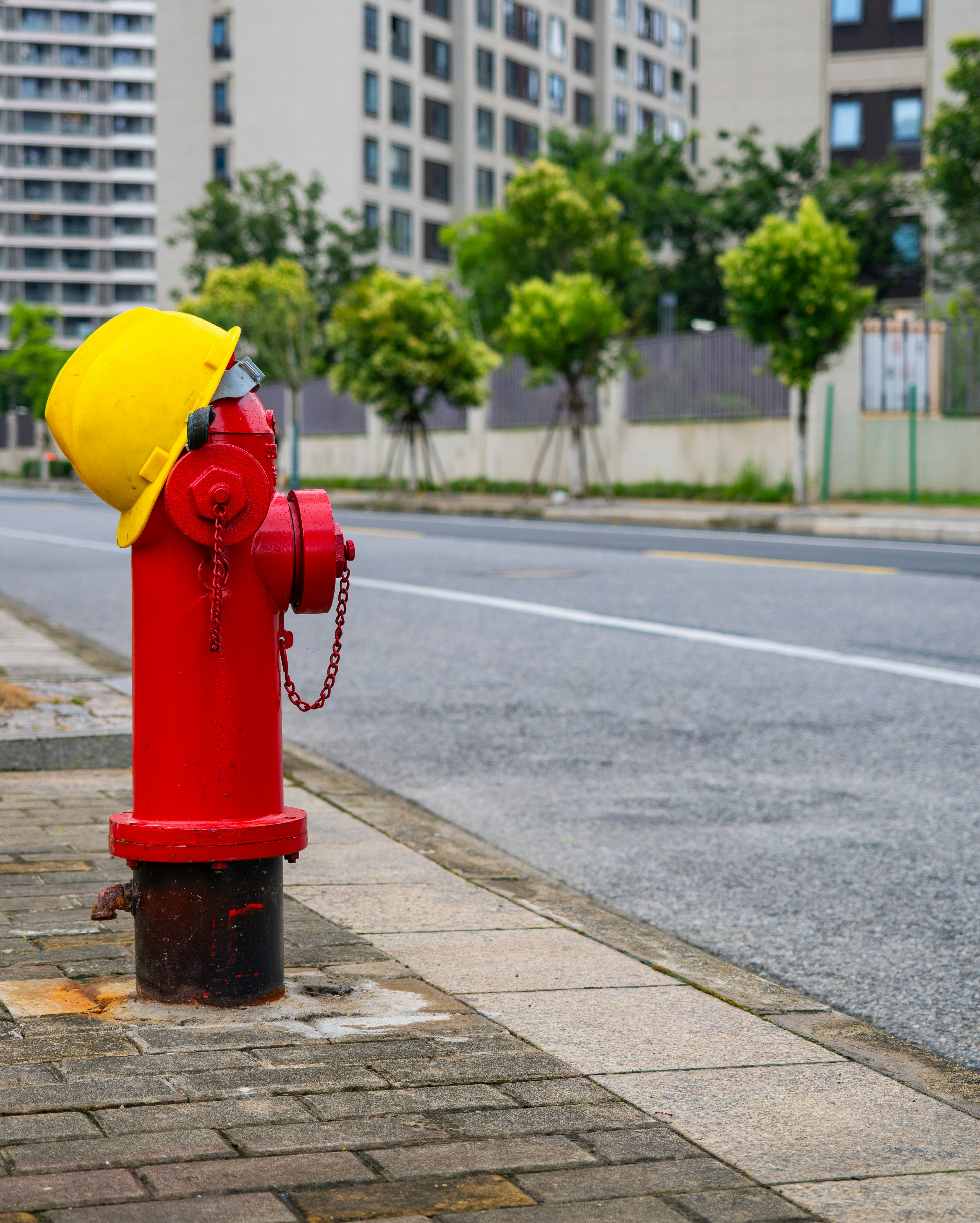 Red Fire Hydrant with Yellow Helmet on a Quiet Urban Street