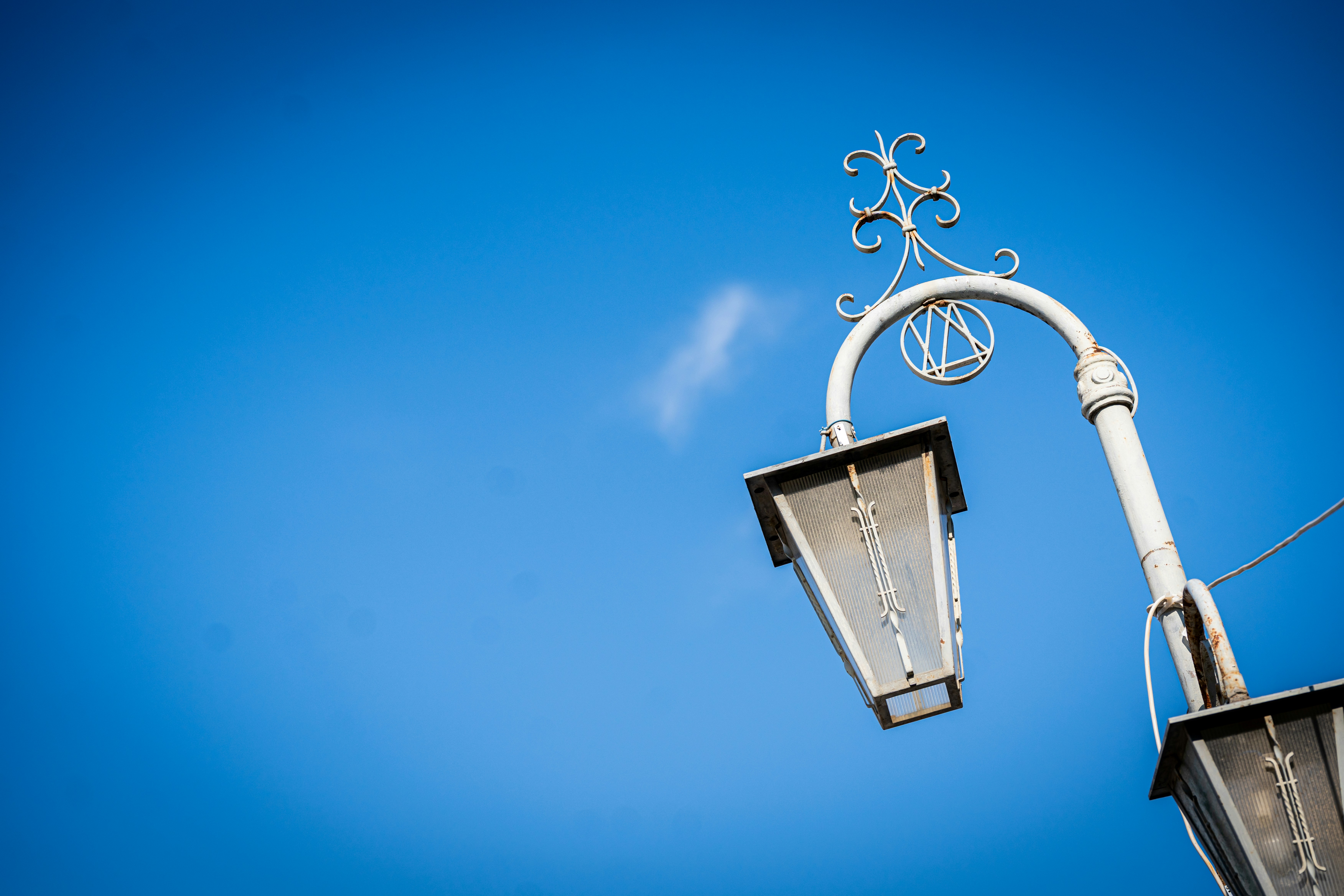Blue Sky and Ornate Lantern: A Skyward View of Vintage Street Lanterns