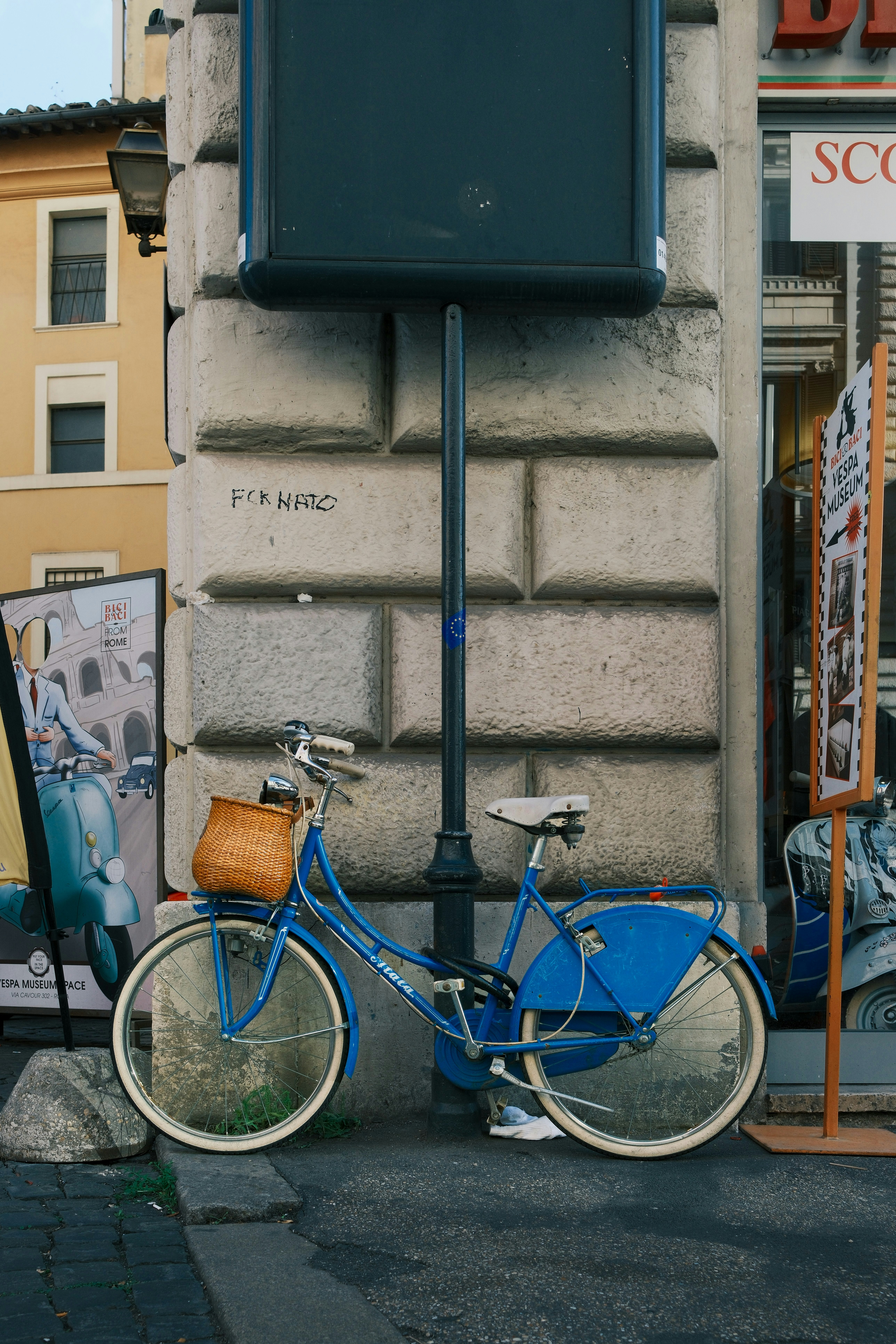 Blue bicycle at the base of a stone building with a cobblestone street