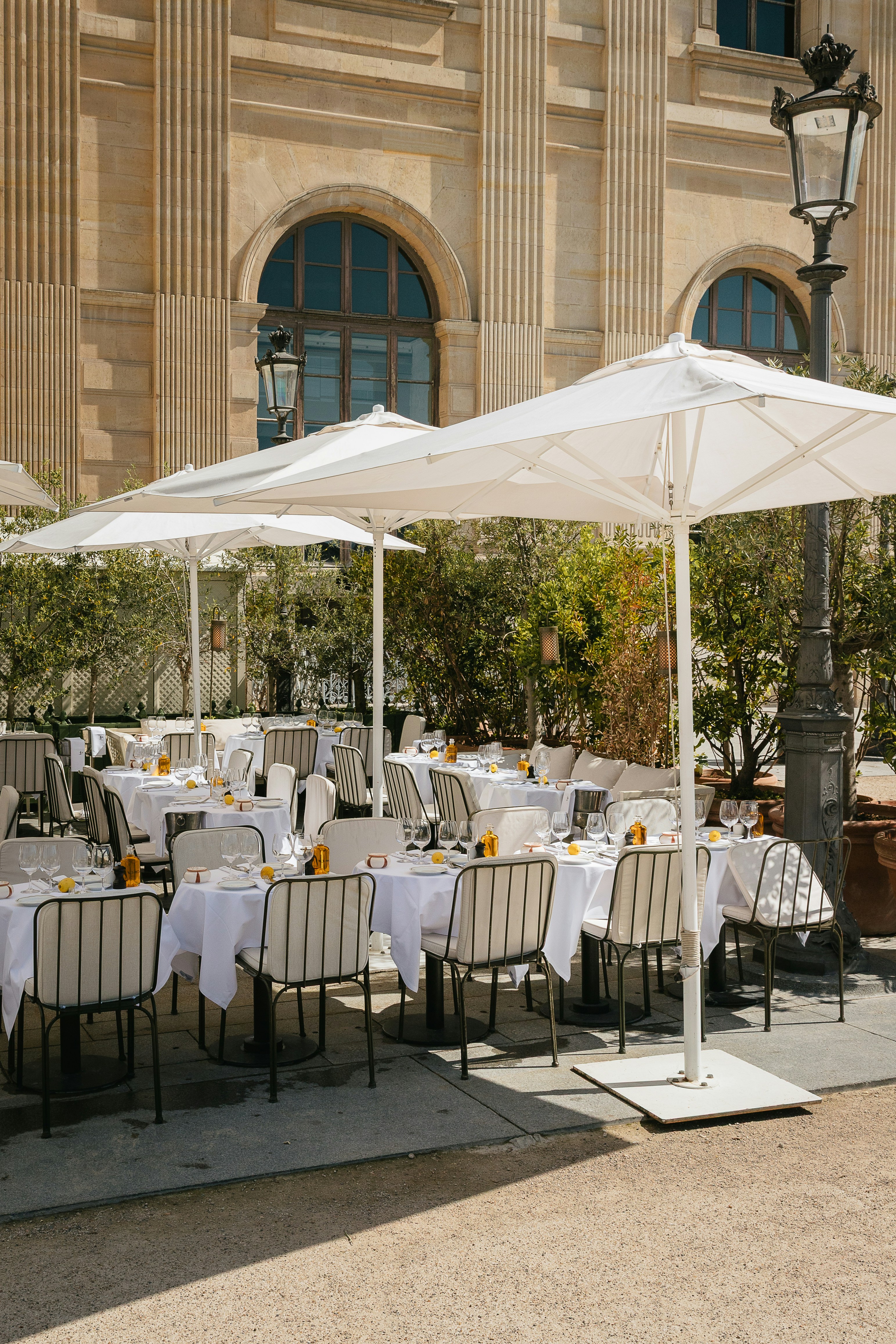 Sunlit Terrace dining under white canopies in front of a historic stone facade