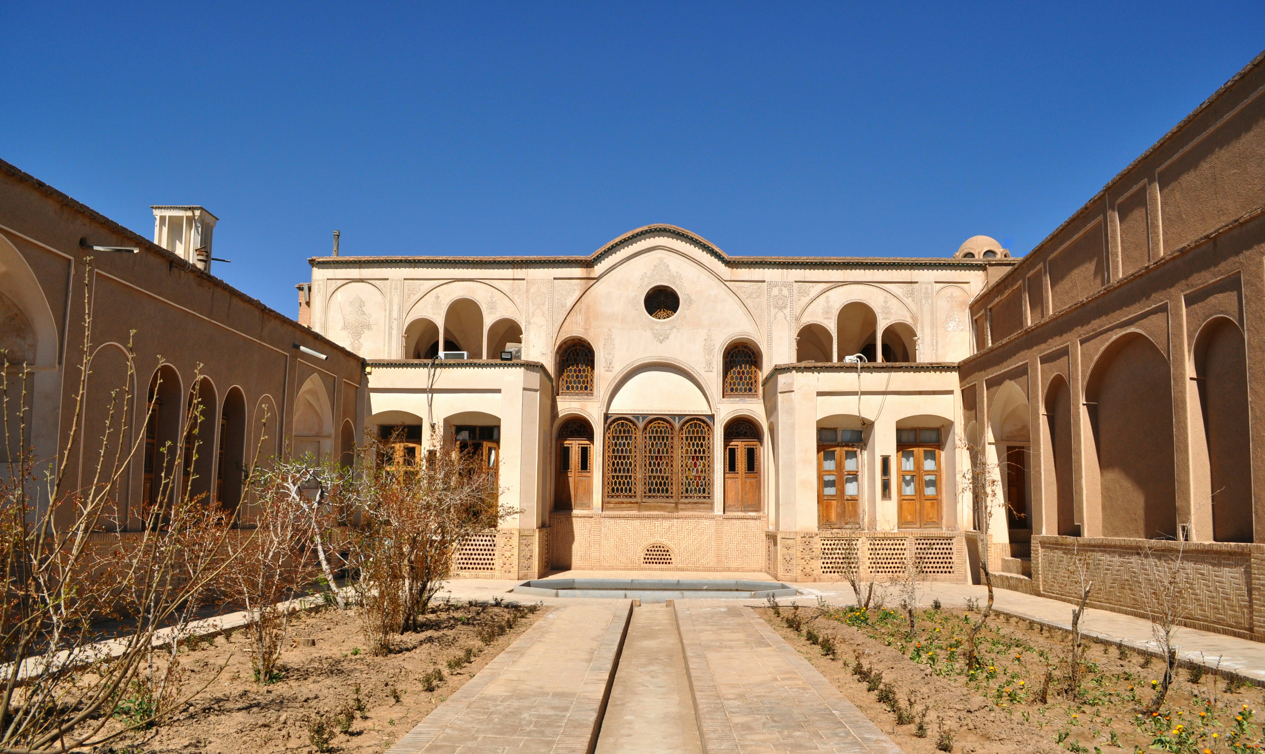 Courtyard Panorama: Sunlit Persian-inspired Facade Framed by Arcaded Wings