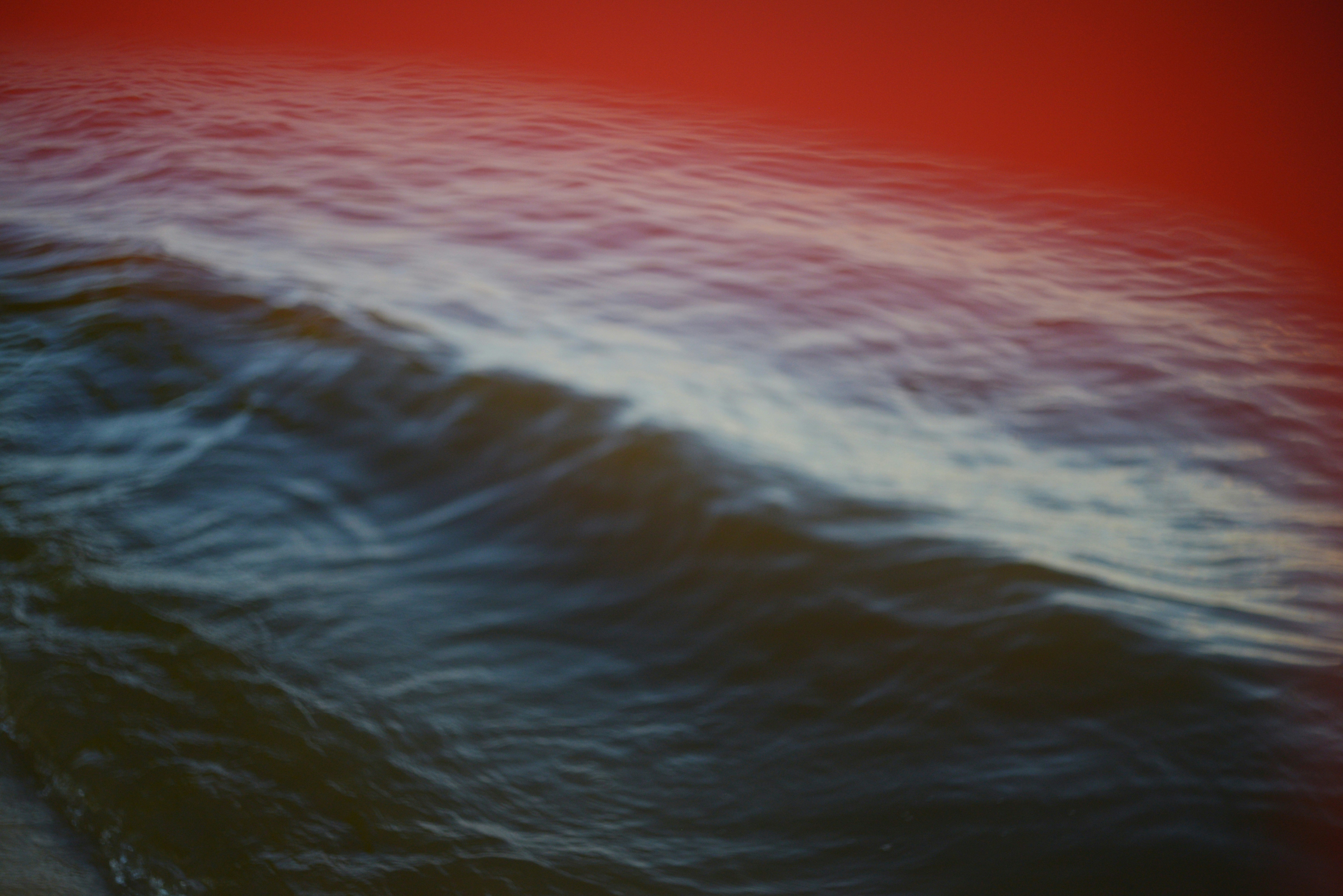 Dark blue-green ocean with a white crest viewed at a slanted angle; red vignette frames the top edge, giving a moody, cinematic feel.