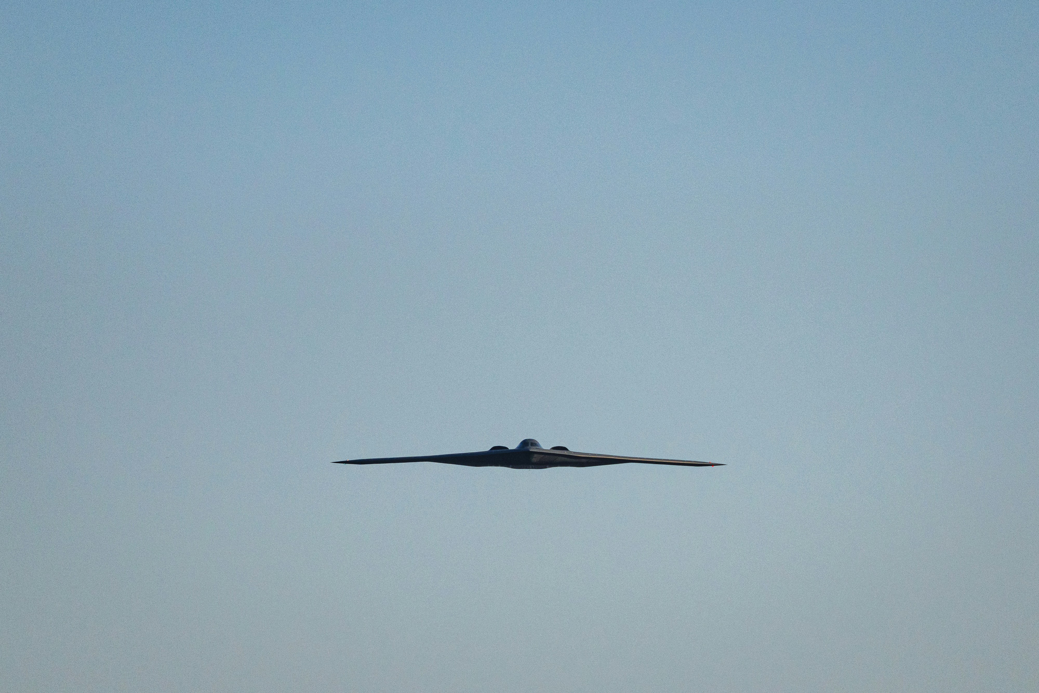 Abstract silhouette of a long, angular aircraft gliding across a pale blue sky; the image isolates the craft in negative space, emphasizing its sleek profile. (Photo is a photography capture.)