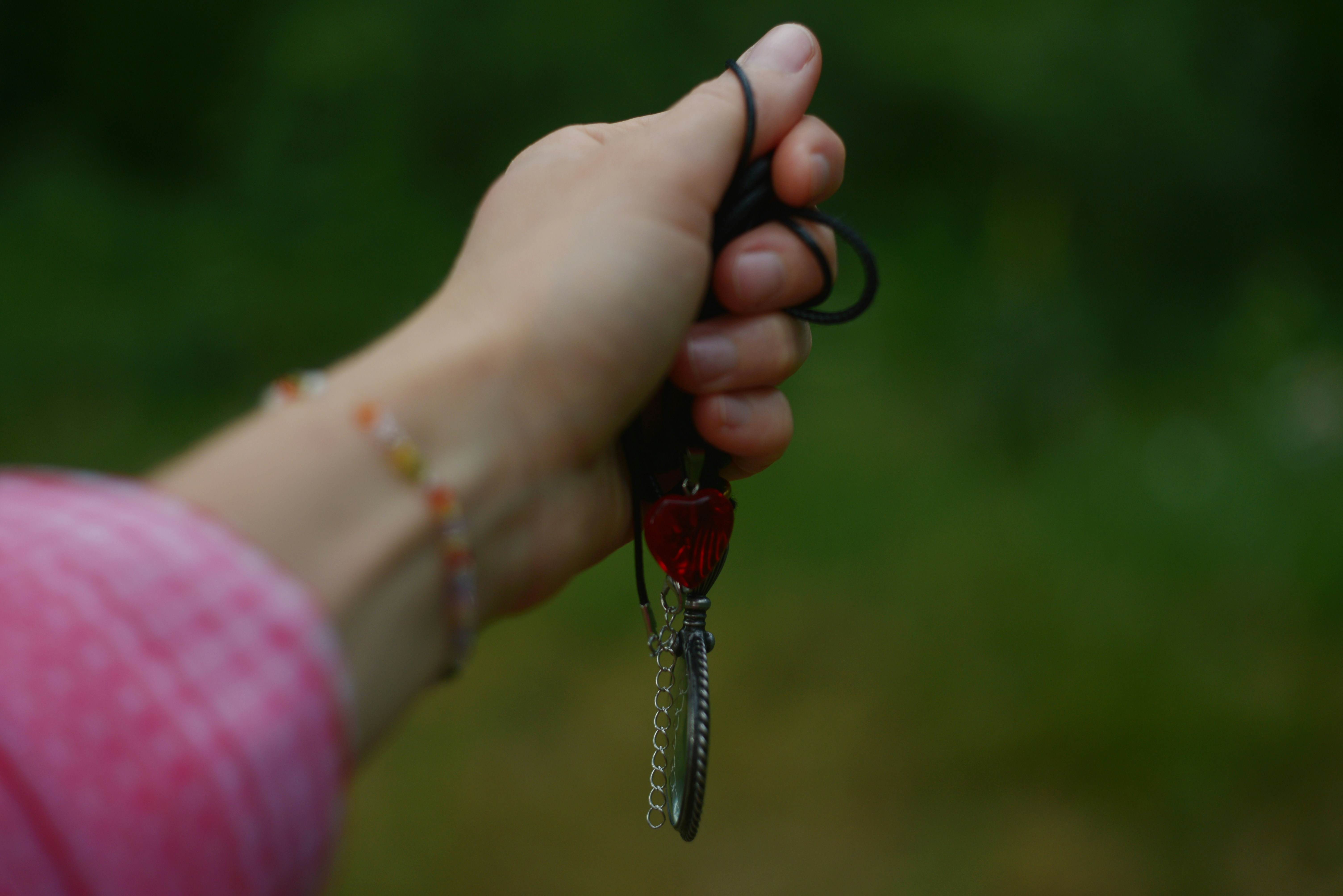 Close-up of a hand firmly gripping a pendant on a keychain, with a blurred natural backdrop and pink sleeve texture in the frame.