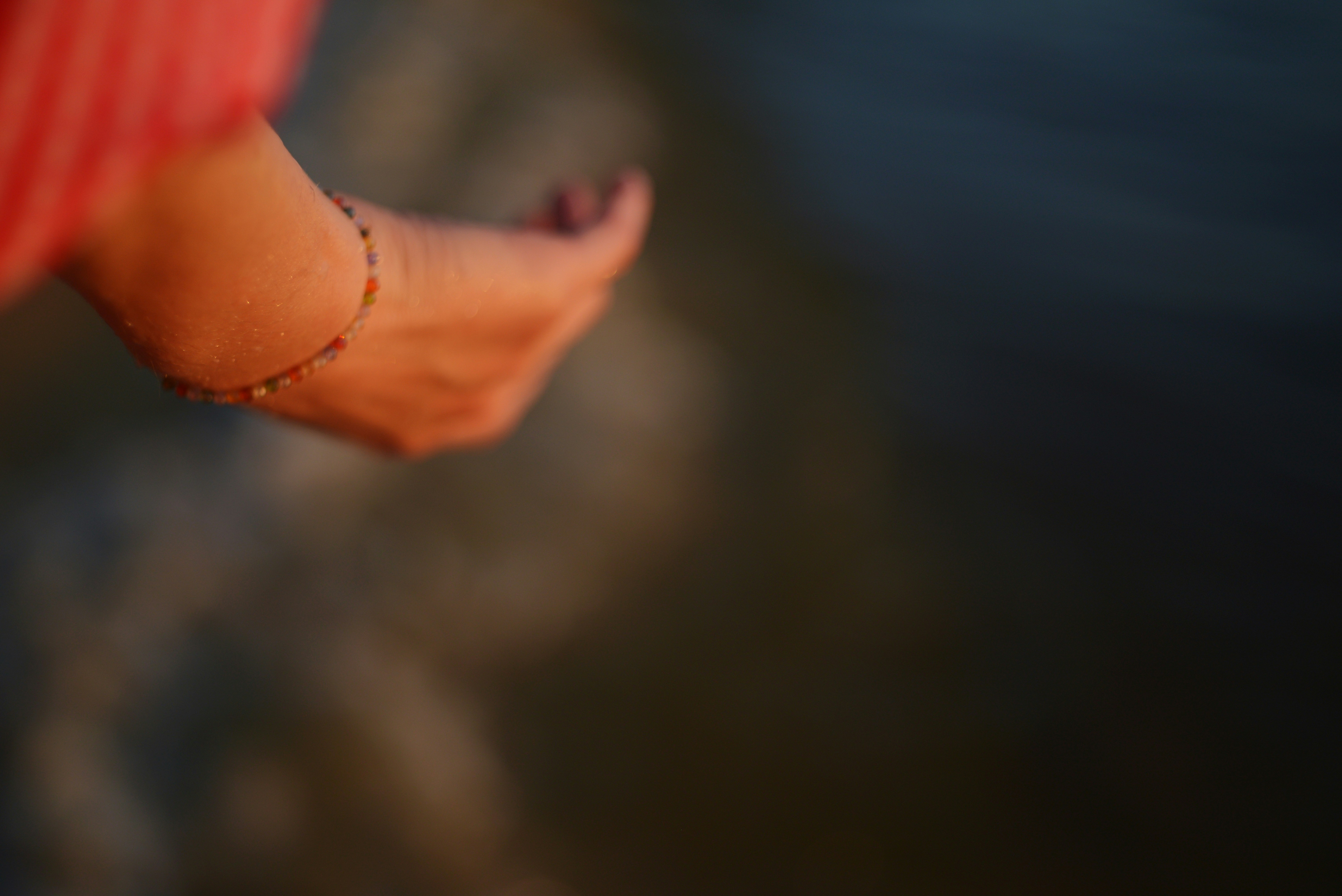 Close-up of a foot dangling over blurred shore and water; a calm, intimate moment focusing on texture and color. This is a candid photograph.
