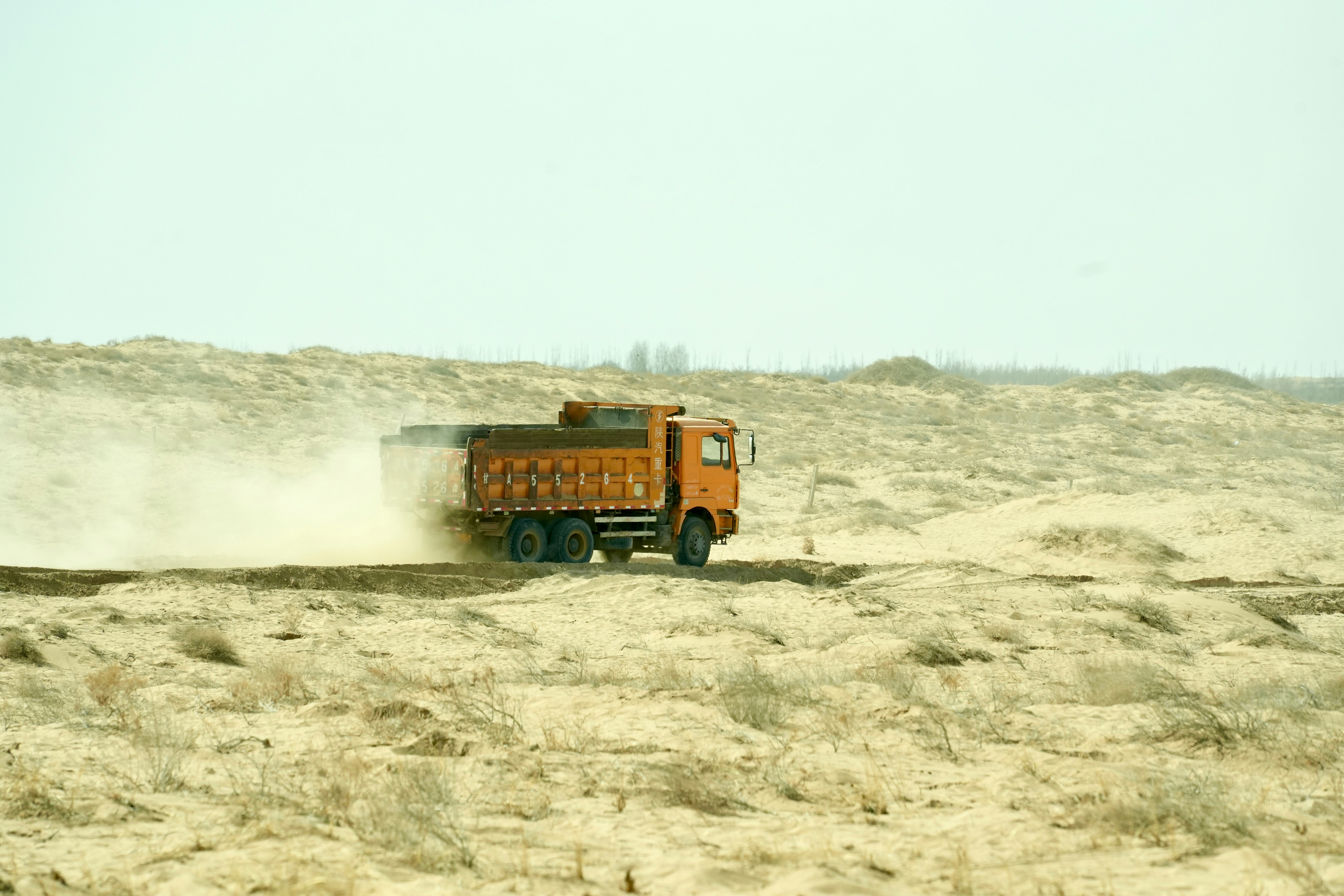 Dust Trail: A solitary orange truck carves a dusty path across a barren desert
