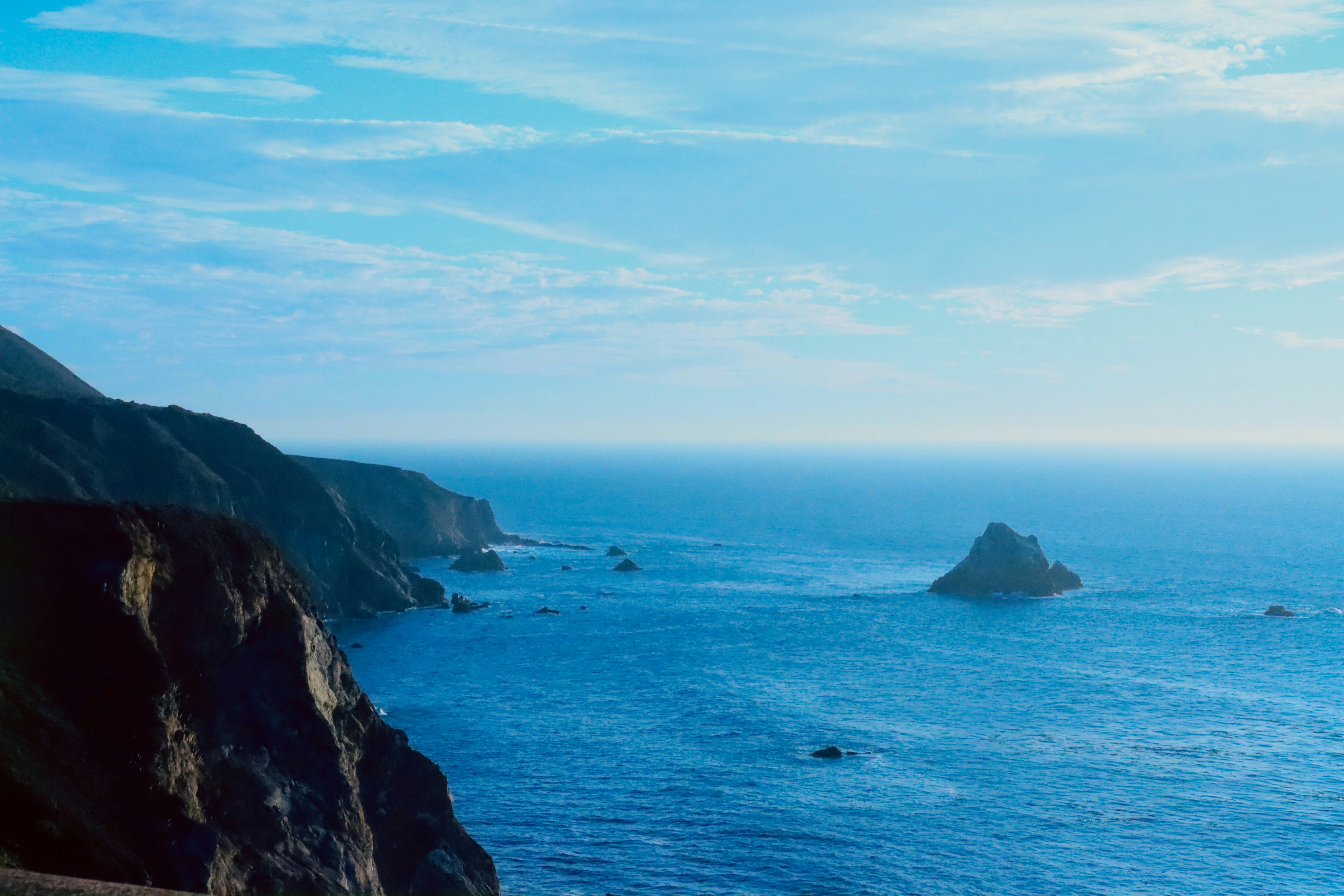 Rugged coastline fades into a calm horizon under a clear blue sky