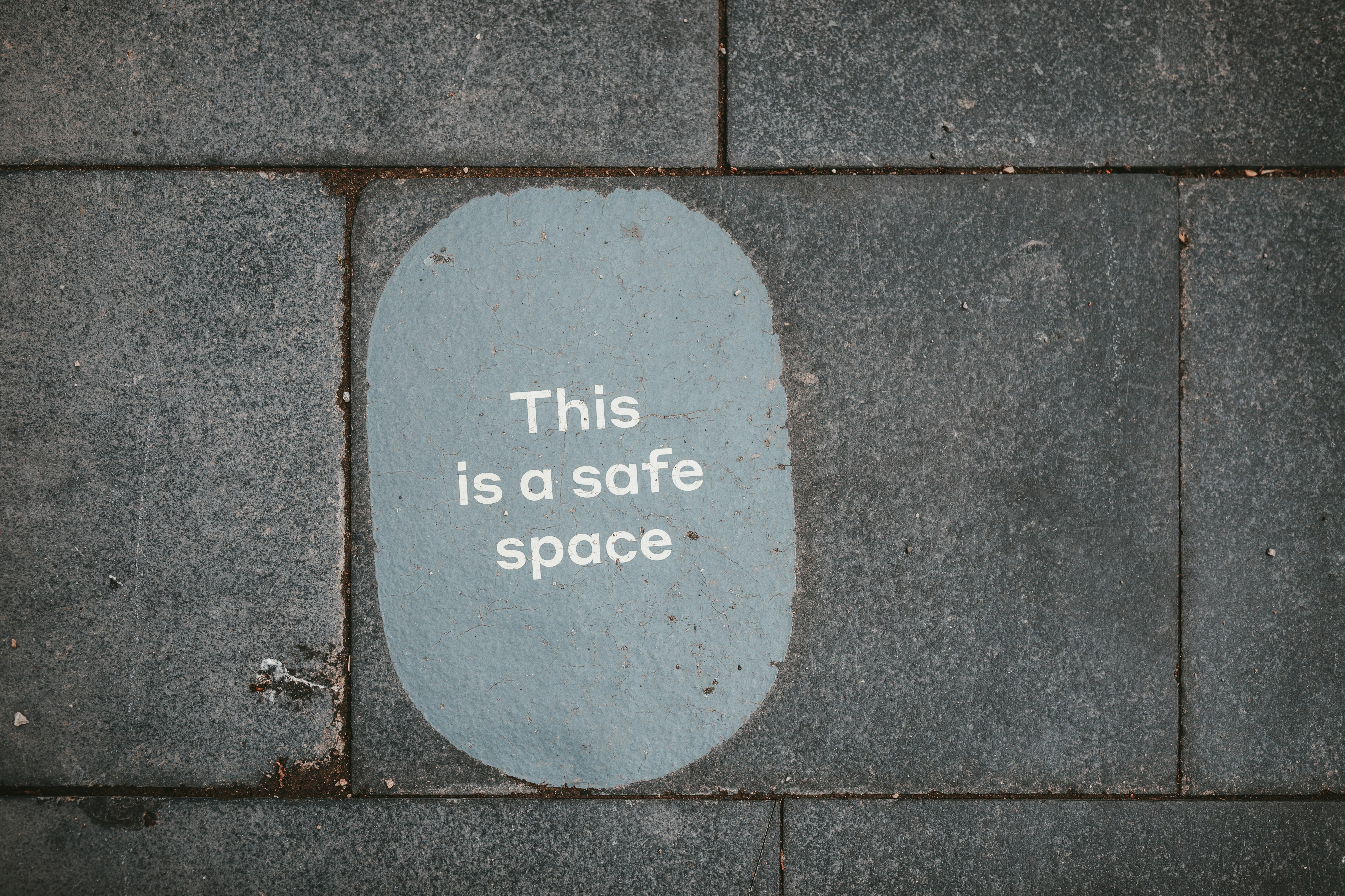 Gray pavement with a pale blue oval containing the words This is a safe space; a subtle street art message on the sidewalk.