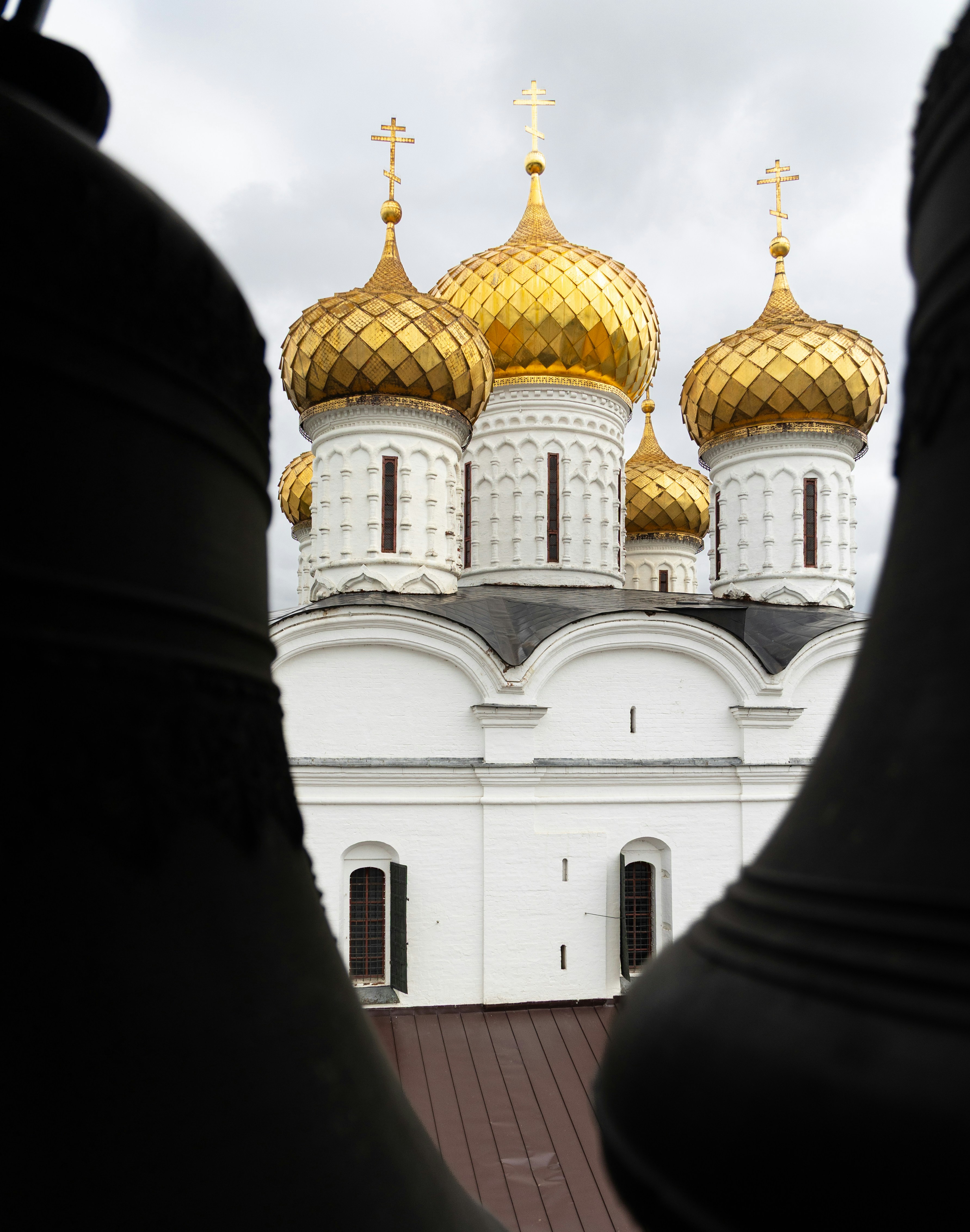 White church walls rise behind dark arch shapes, showcasing the golden onion domes framed as if viewed through a doorway.