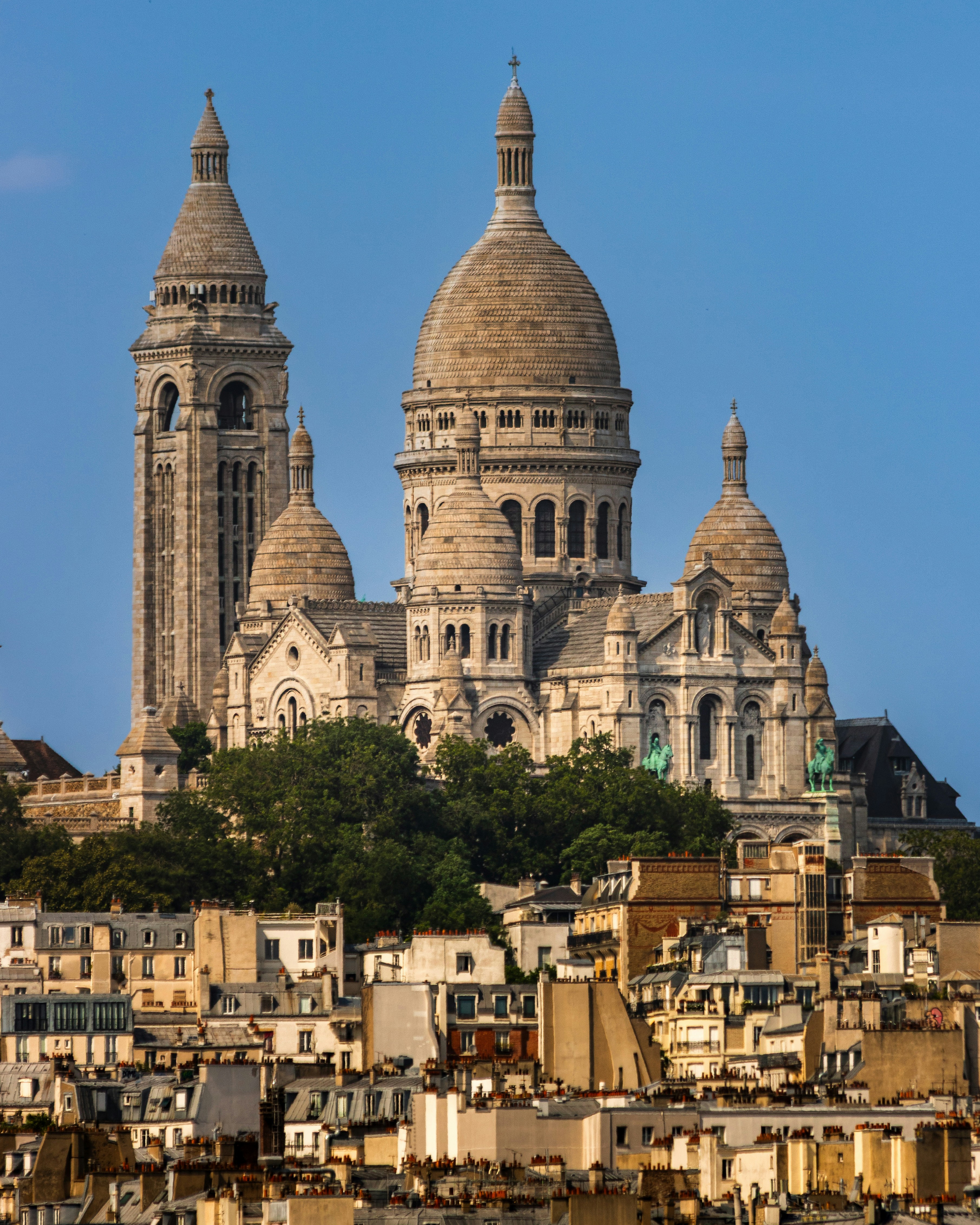 Vue urbaine du Sacré-Cœur dominant le quartier de Montmartre avec ciel bleu pendant la journée; architecture religieuse et bâtiments historiques en contrebas.