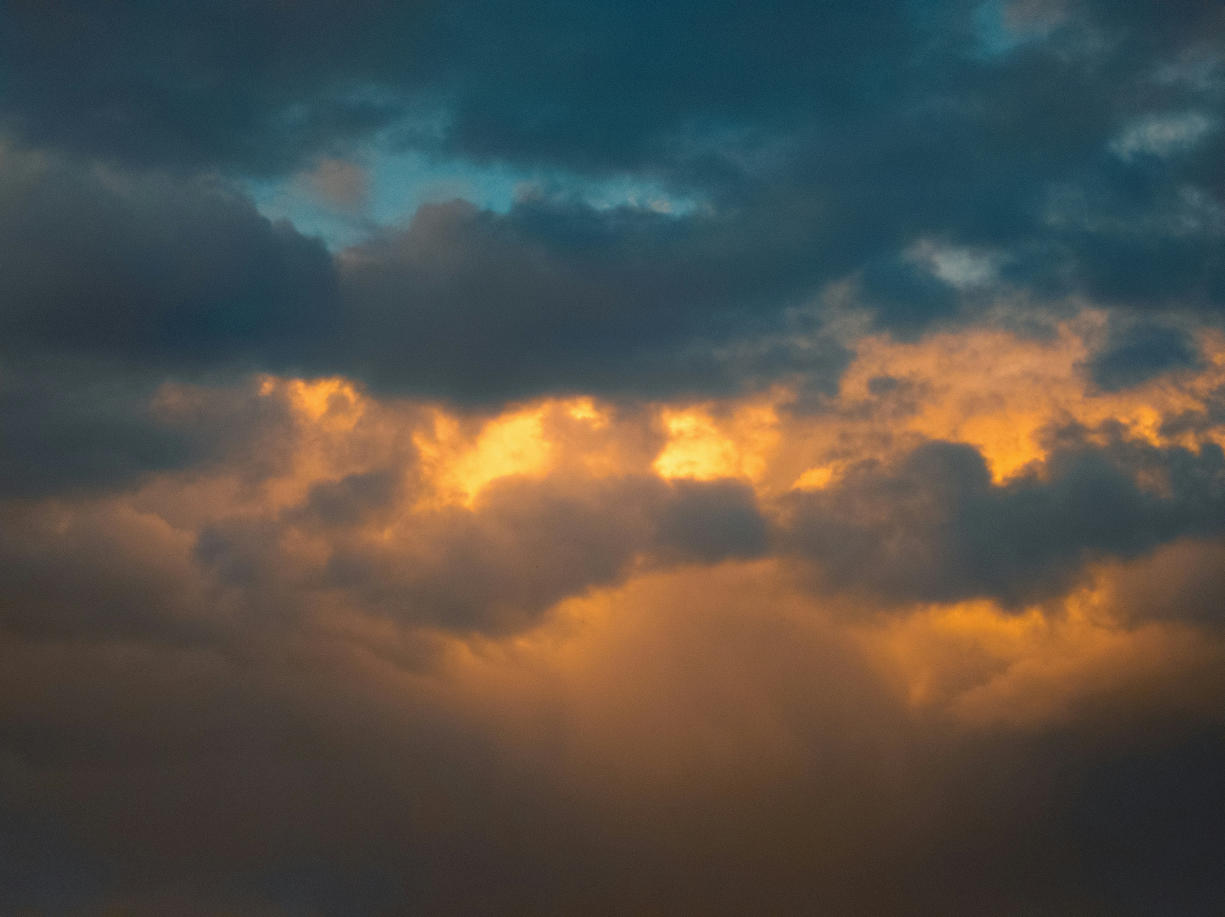 Golden sunlight pierces a cloud deck, casting warm beams across a moody sky.