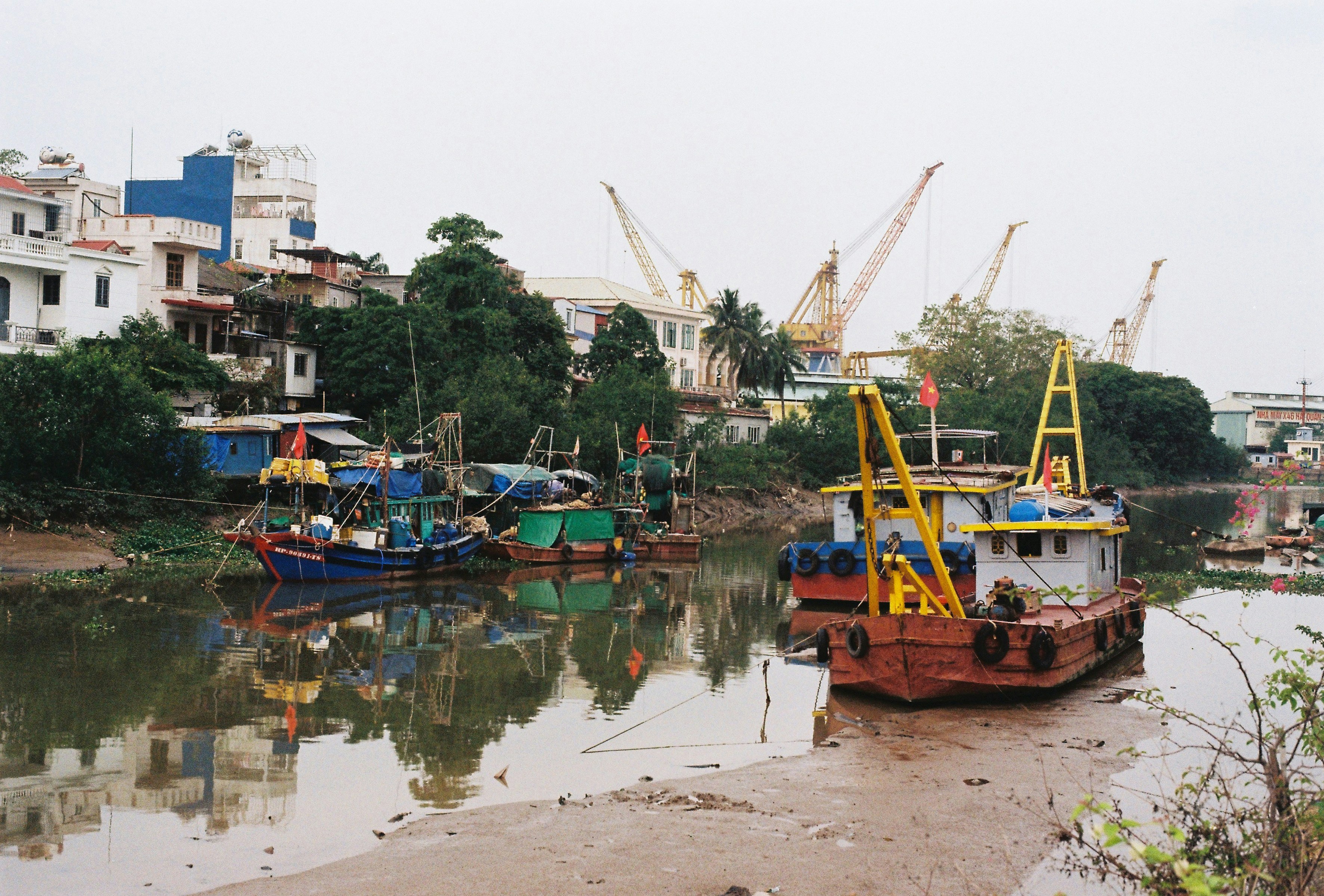 Harbor stillness: boats and cranes at dusk-lit riverbank