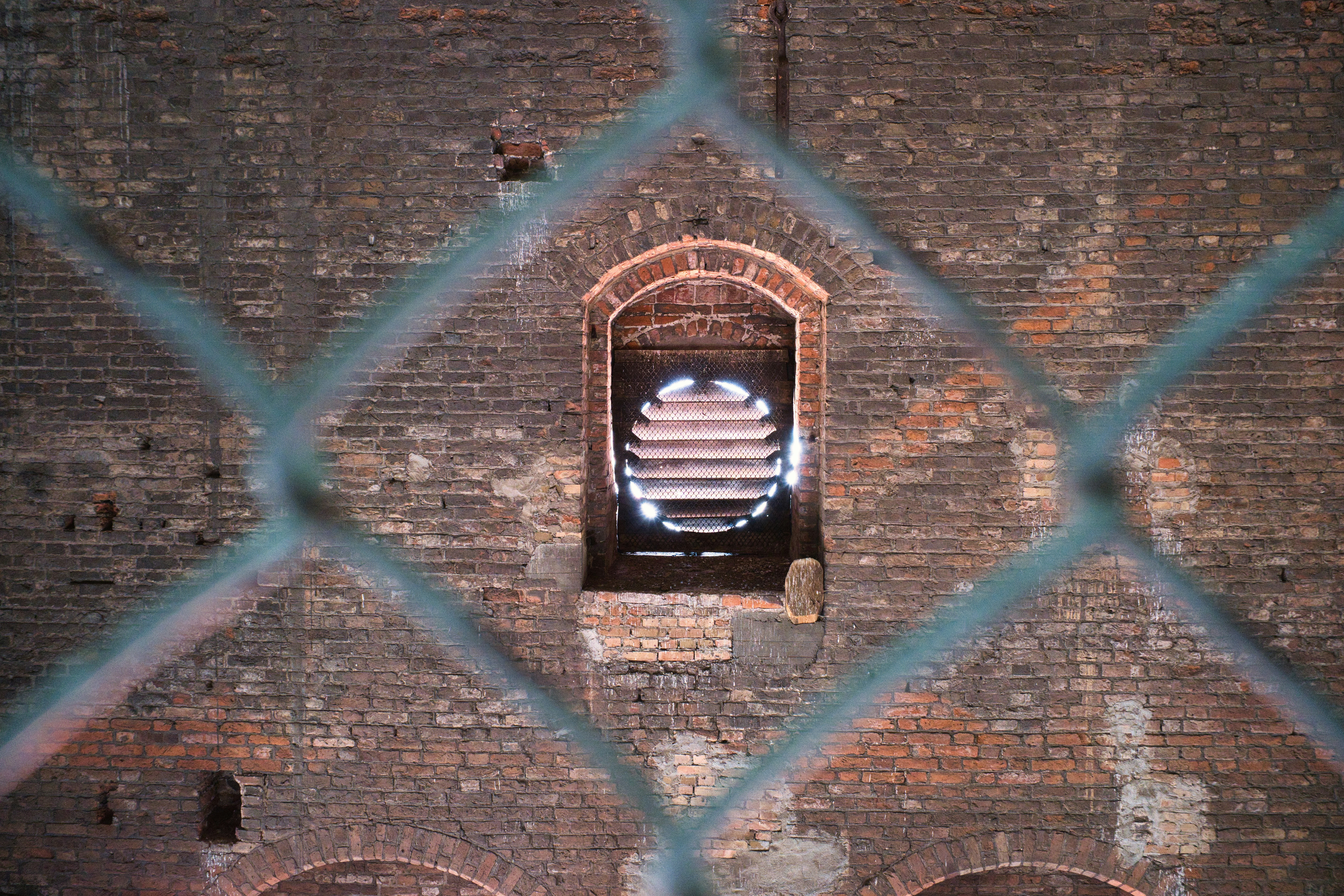Through the Brick Veil: A Distant Stairwell Framed by Chain Link