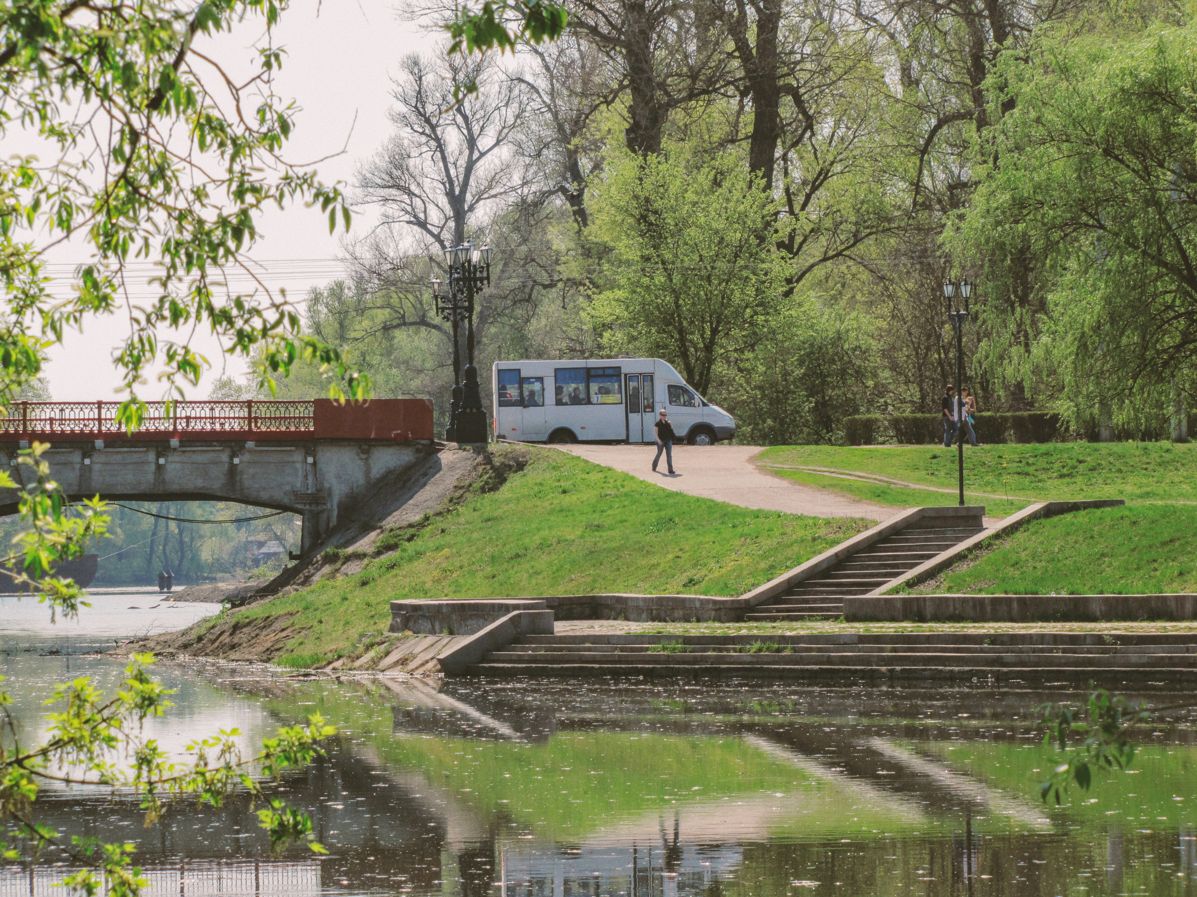 White van on a park path beside a calm river