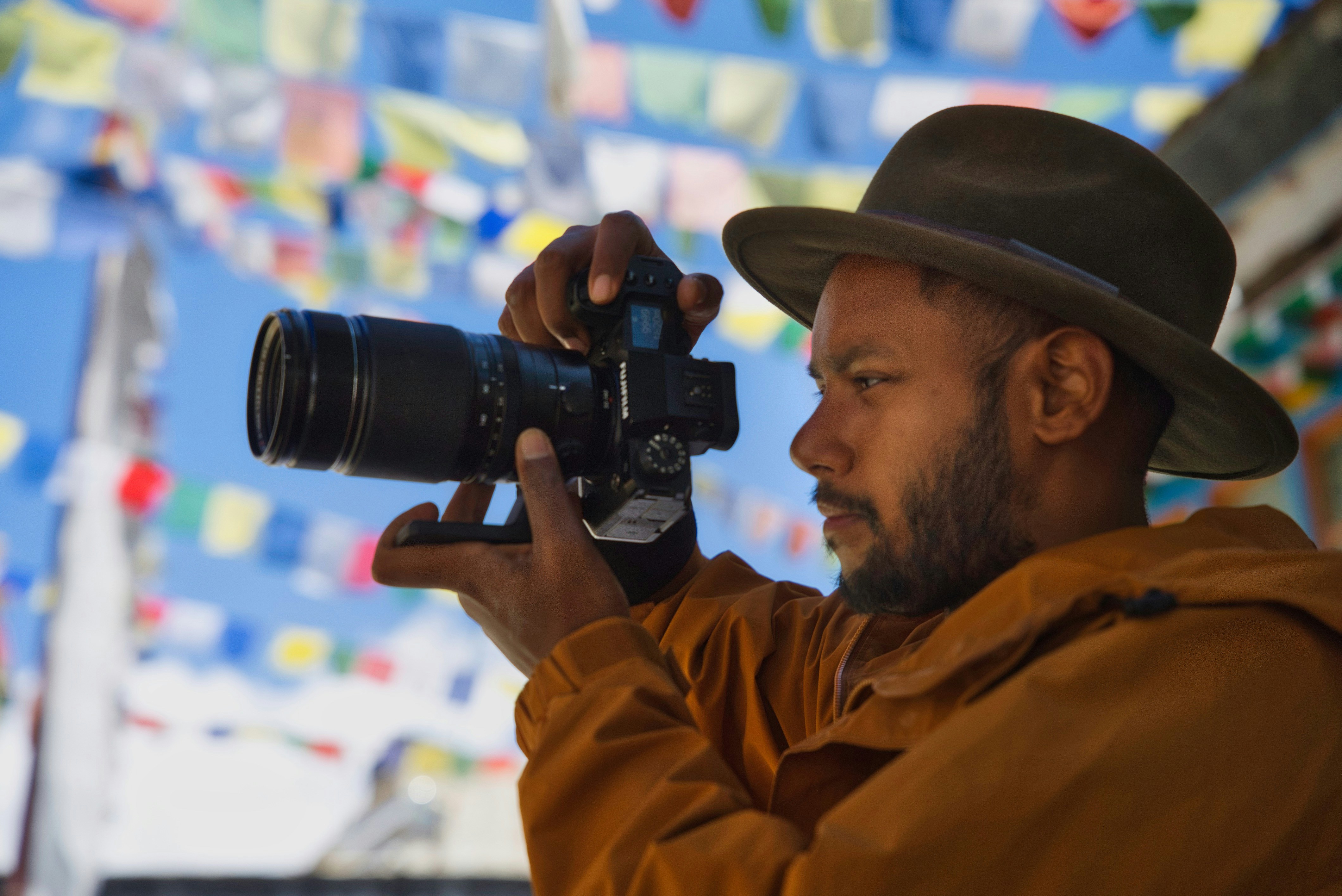 Photographer with a camera in hand, under vibrant prayer flags, capturing a moment of focus and concentration.