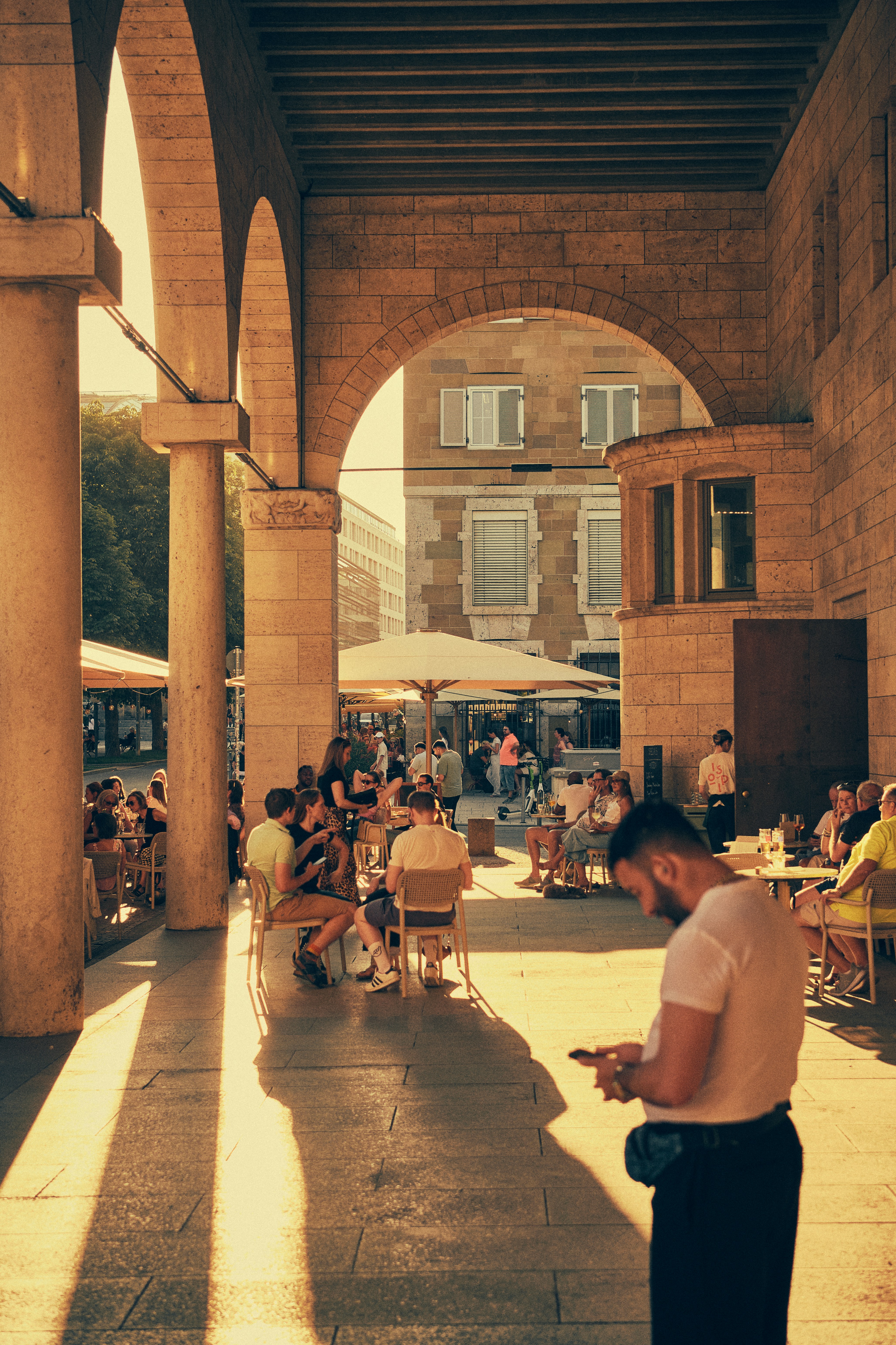 Sunlit Terrace Rally: People Gather Under Arches in a Warm Piazza