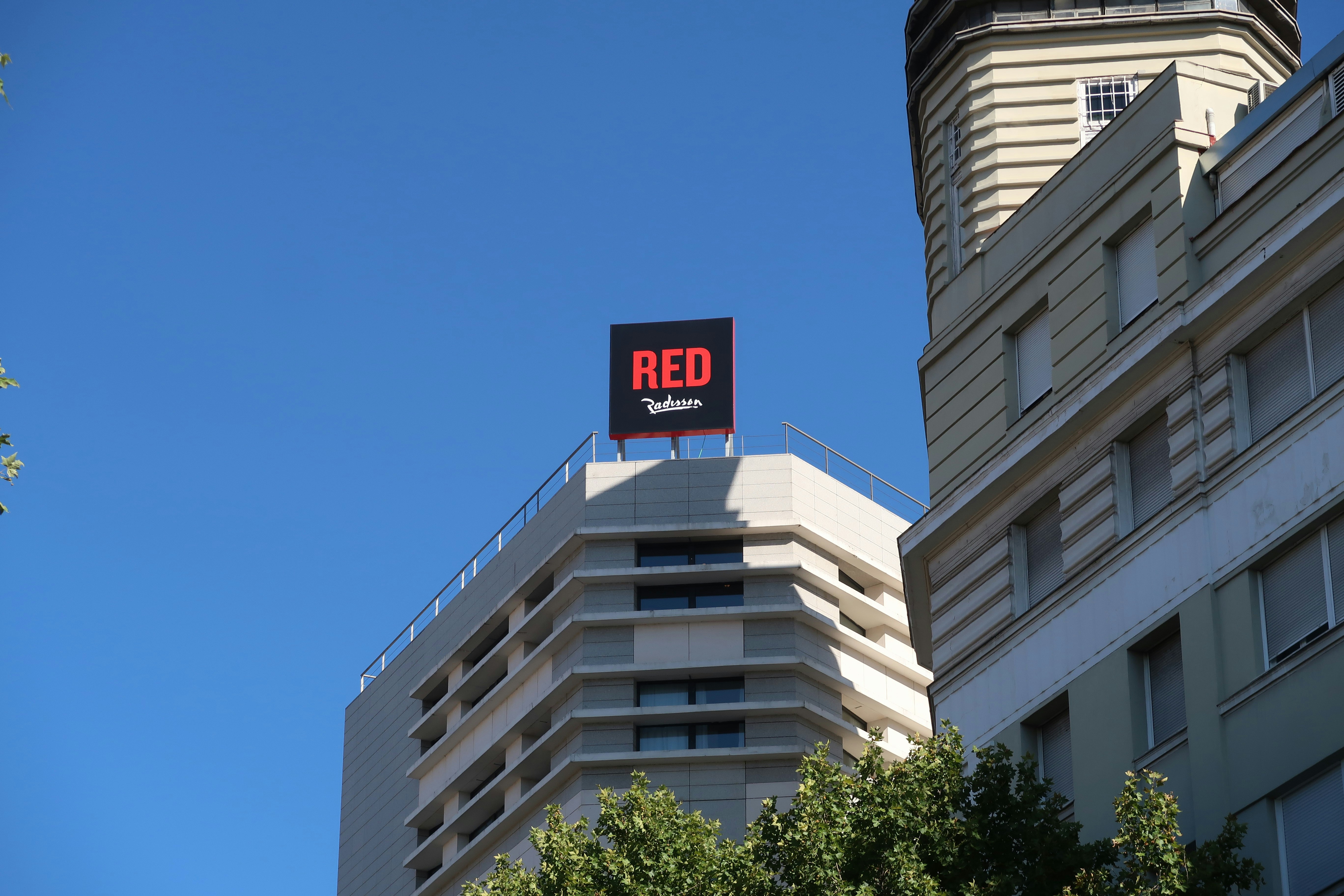 Red Sign atop a modern corner building against a clear blue sky