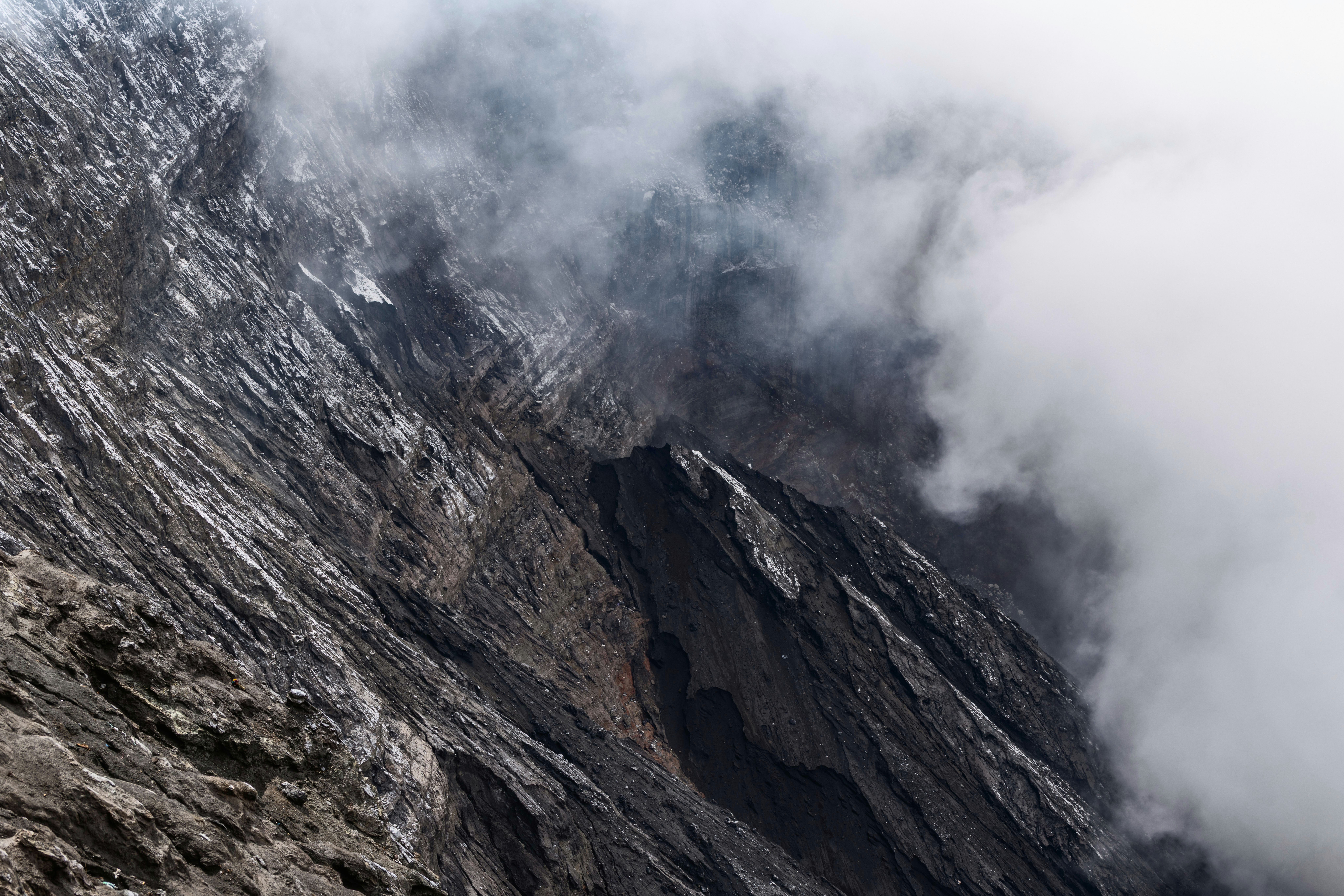 Rugged rock faces rise through a veil of low clouds, revealing angular striations and a moody alpine atmosphere. A minimalist landscape emphasizing texture and depth.