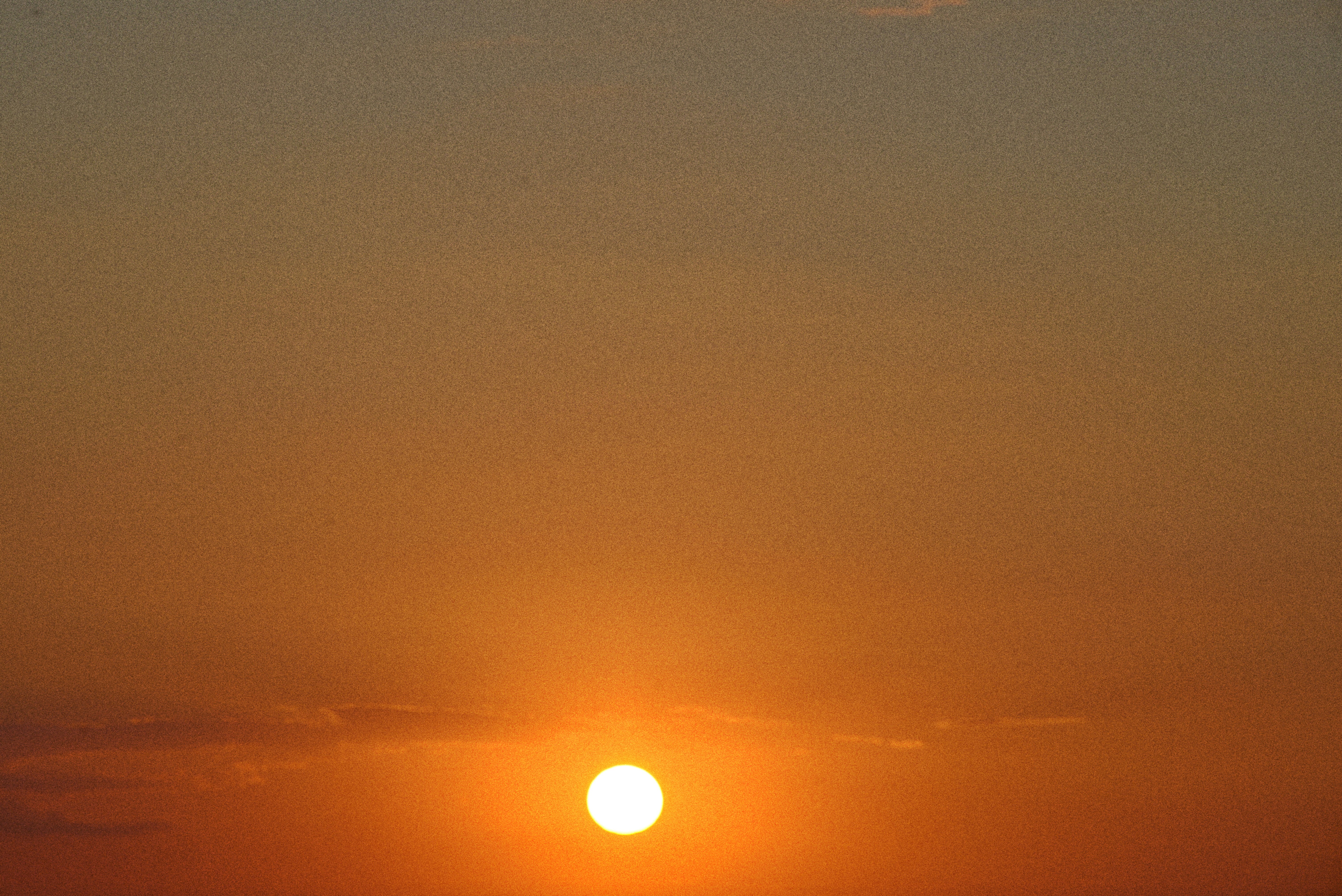 Golden sun sits low on an orange horizon, casting warm tones across a calm sky. A minimal landscape scene captured at dusk.