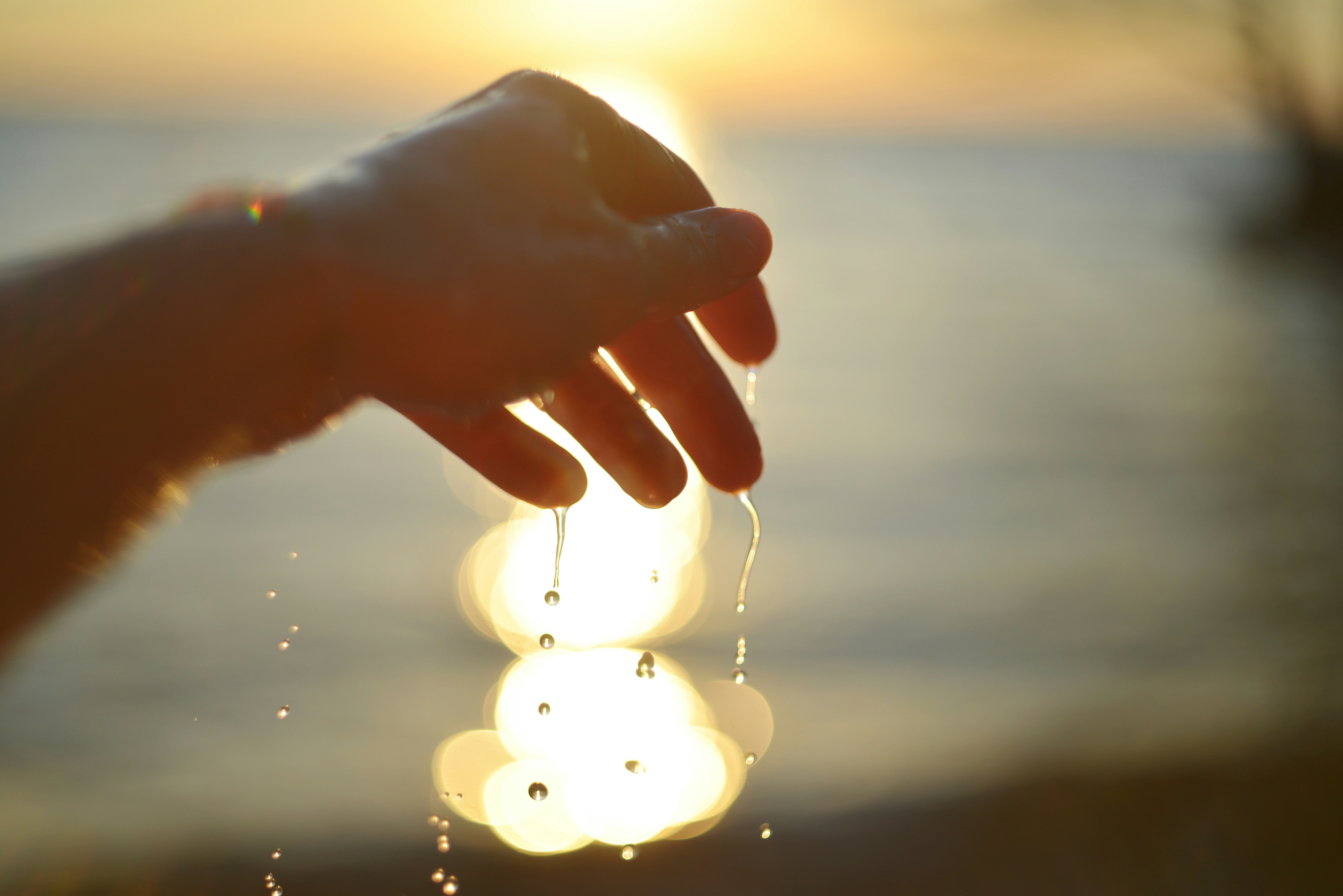 Sunlit droplets: a hand releasing light at sunset over water