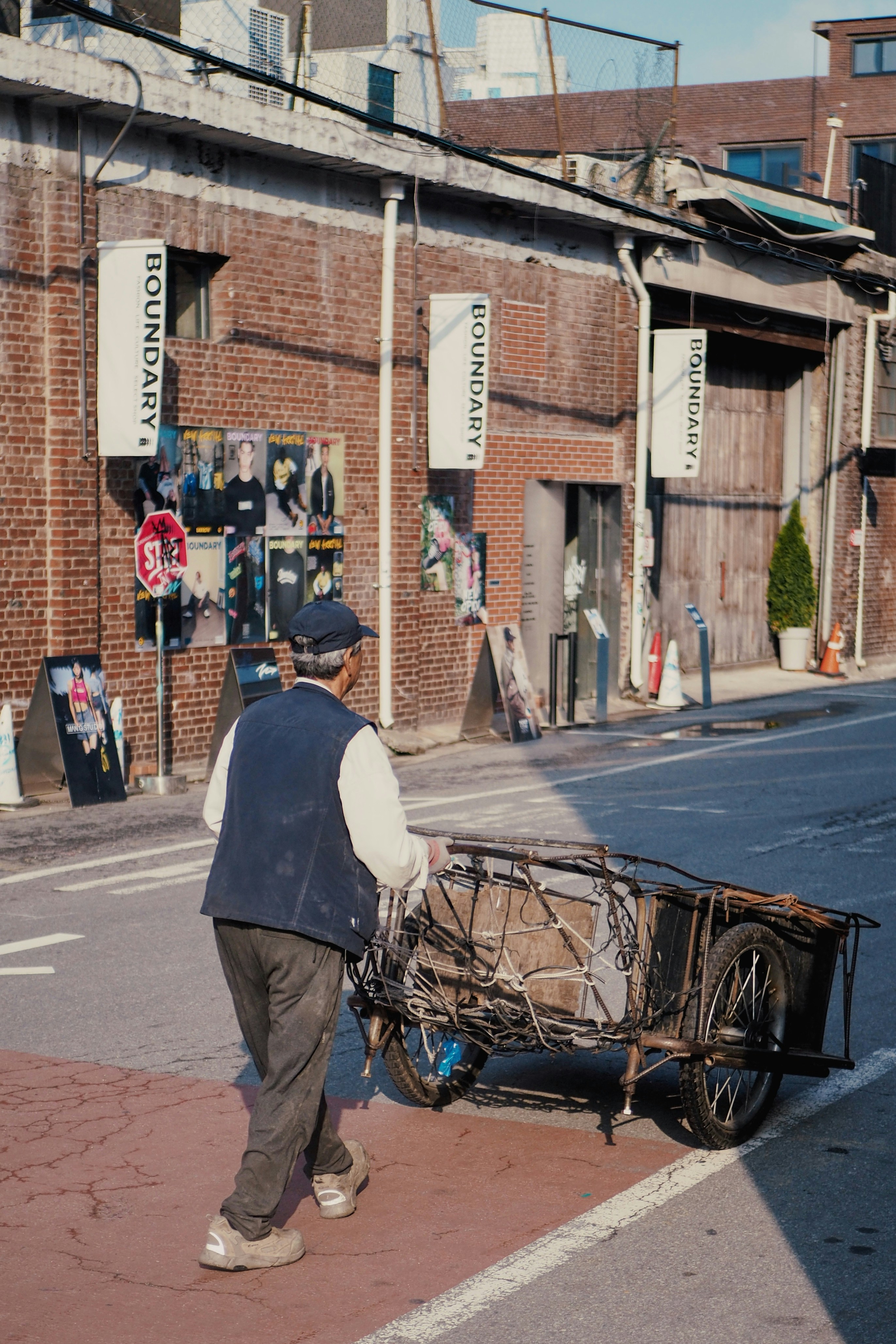 Overloaded bystander: a street cart and a determined walker in a brick-lined shop row