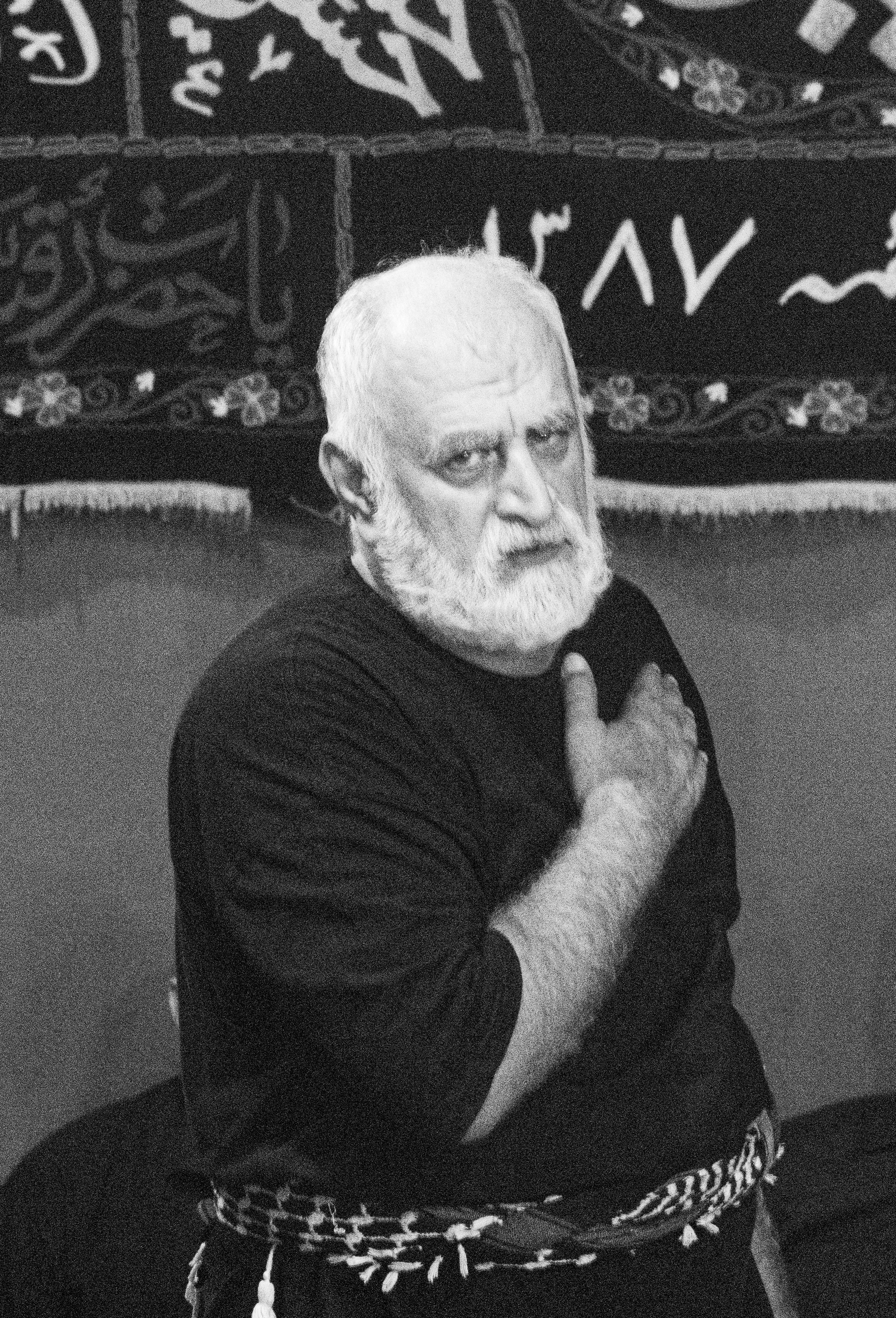 An attentive elder with a solemn gaze, seated before a patterned backdrop