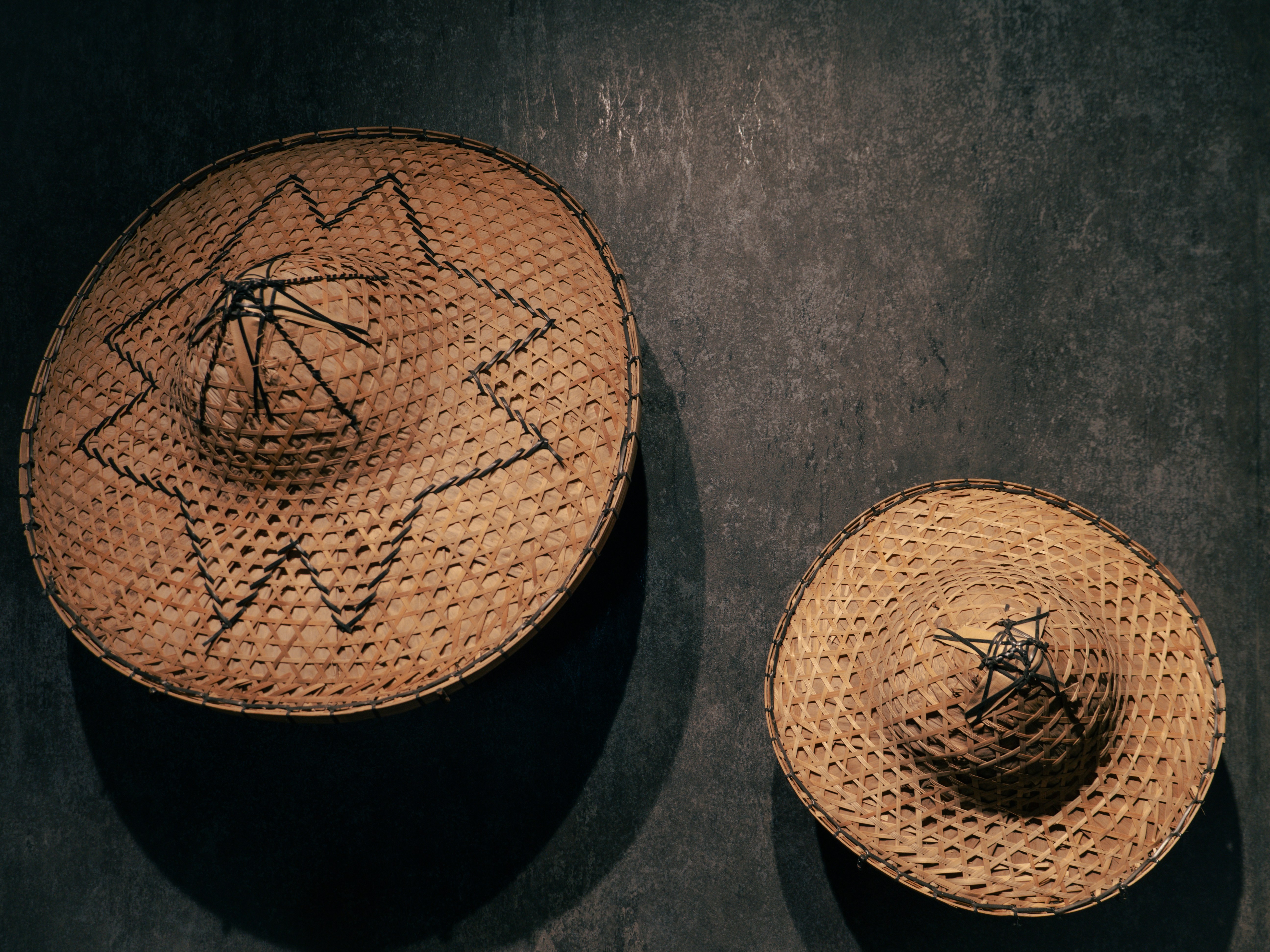 Woven Shadows: Two Straw Hats Against a Dark Wall